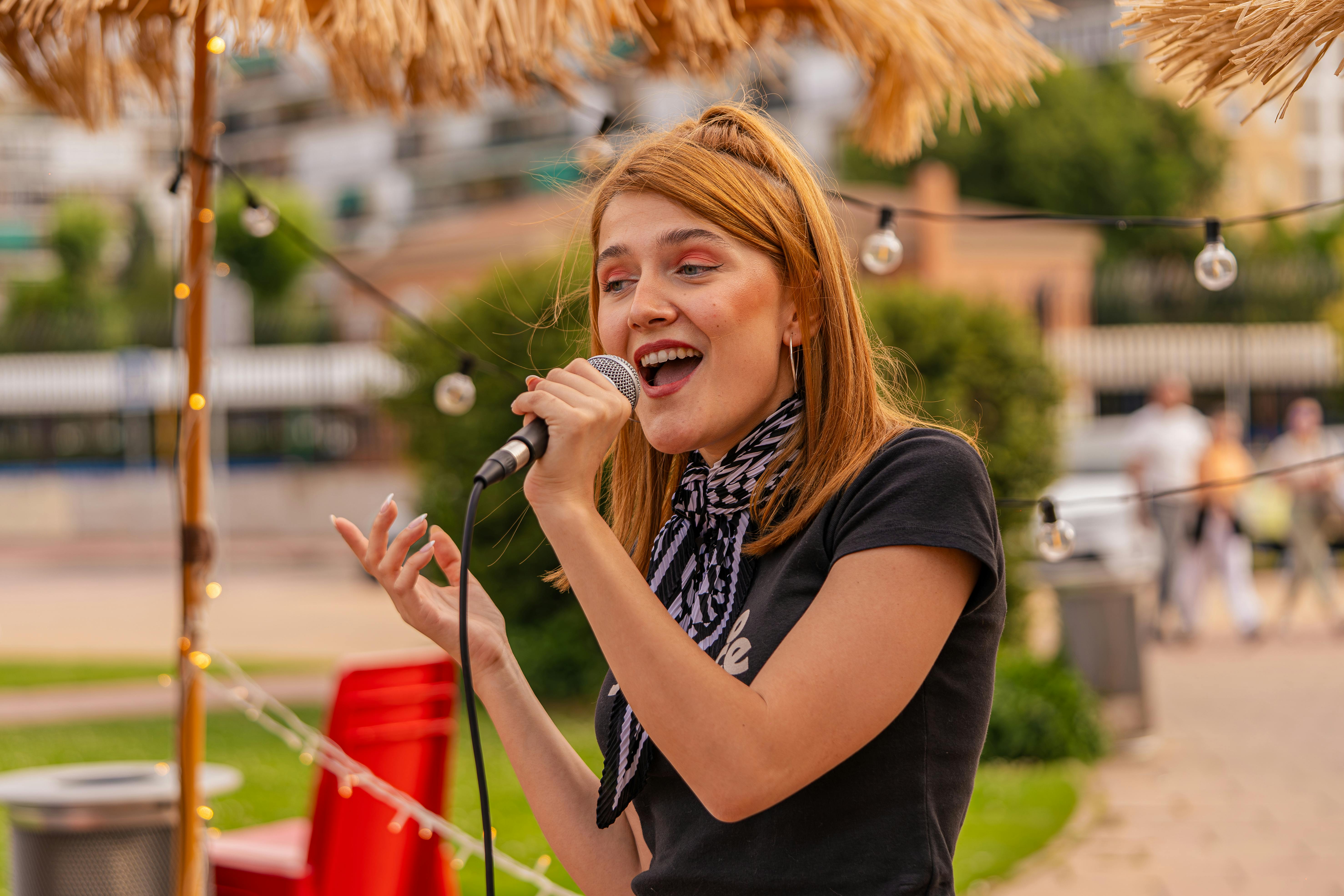 Young Redhead Woman Singing on Stage with Straw Umbrellas · Free Stock ...