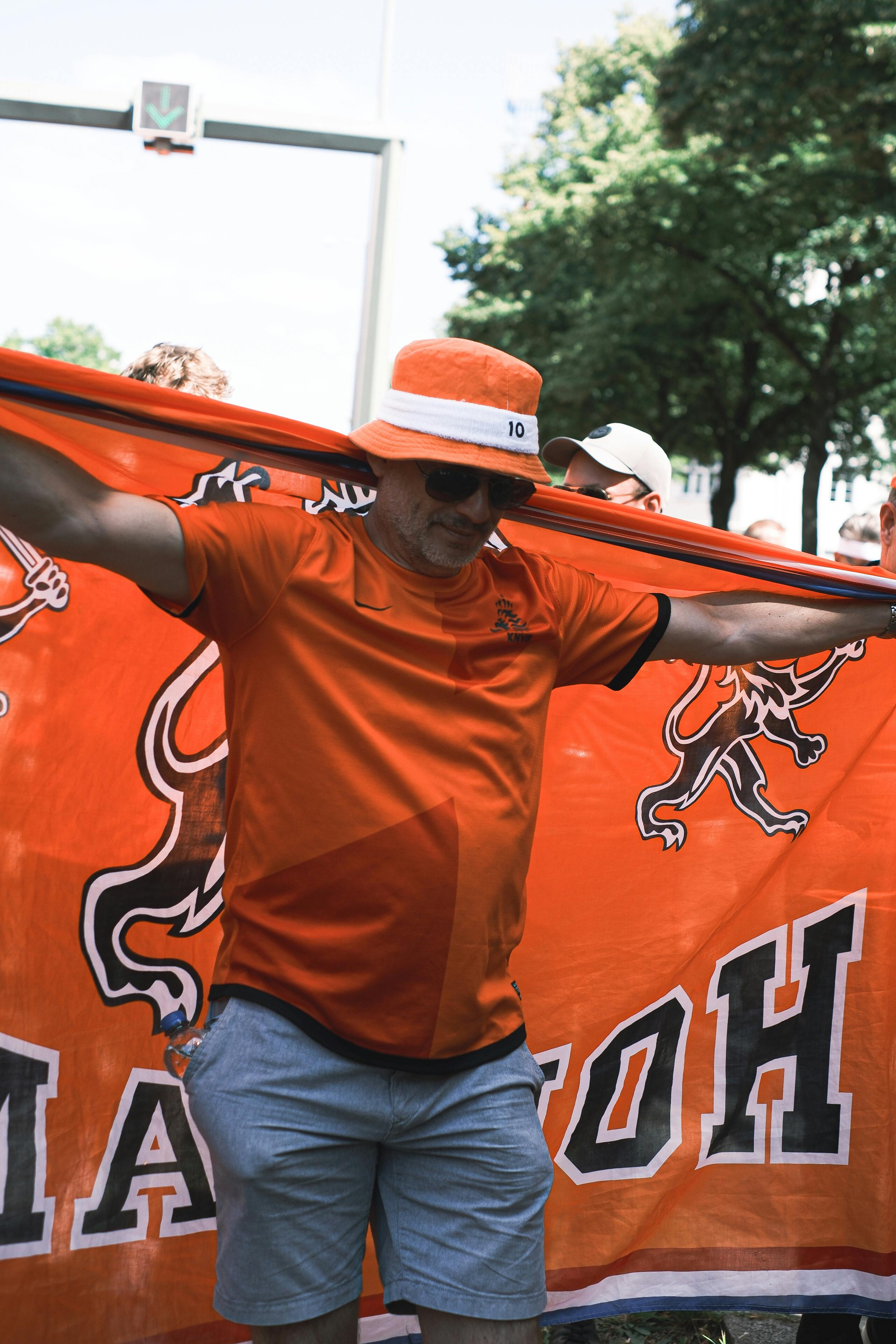 A man in an orange shirt holding up a large orange and white flag ...