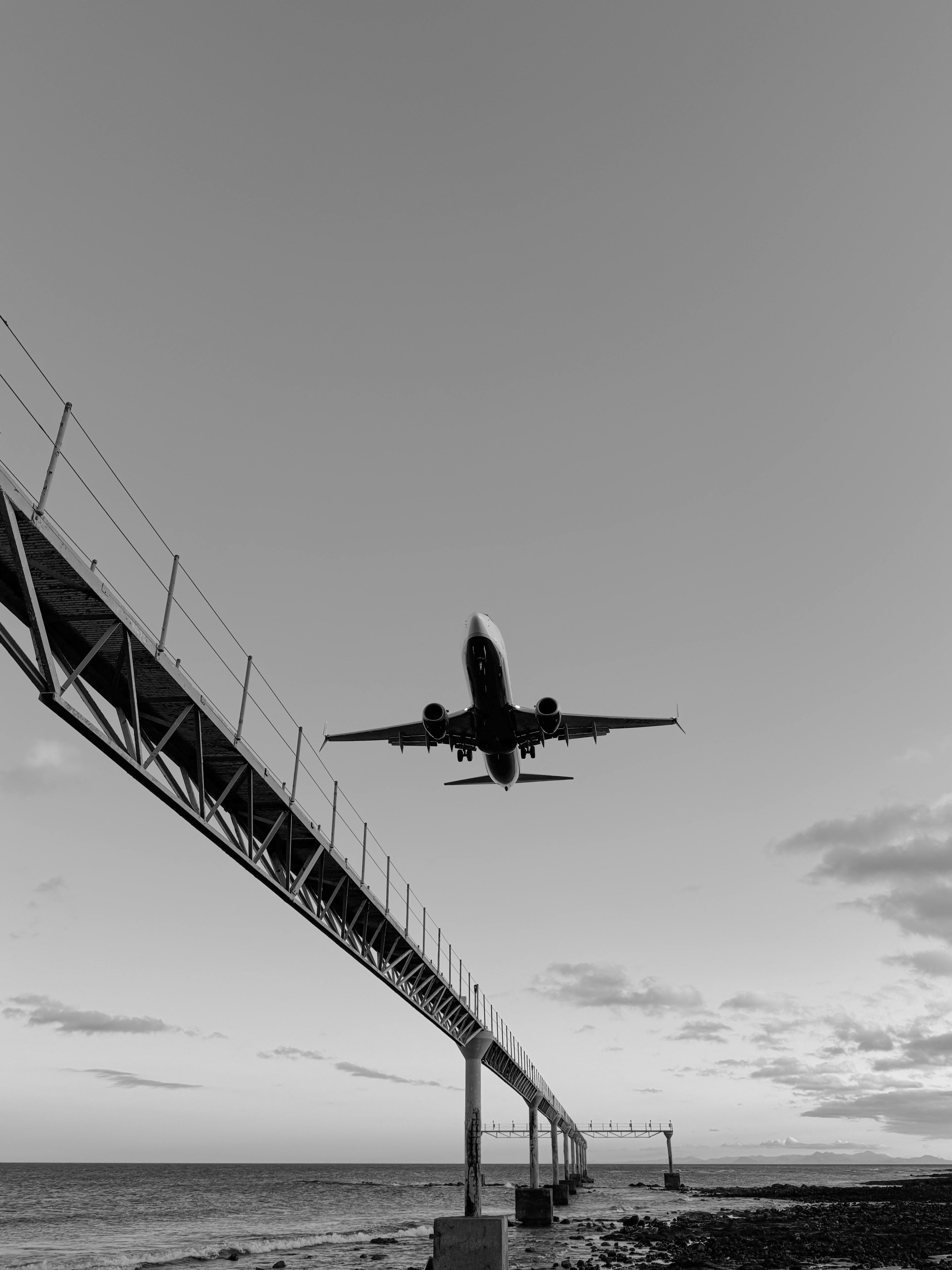 Airplane Flying over Bridge on Sea Coast · Free Stock Photo