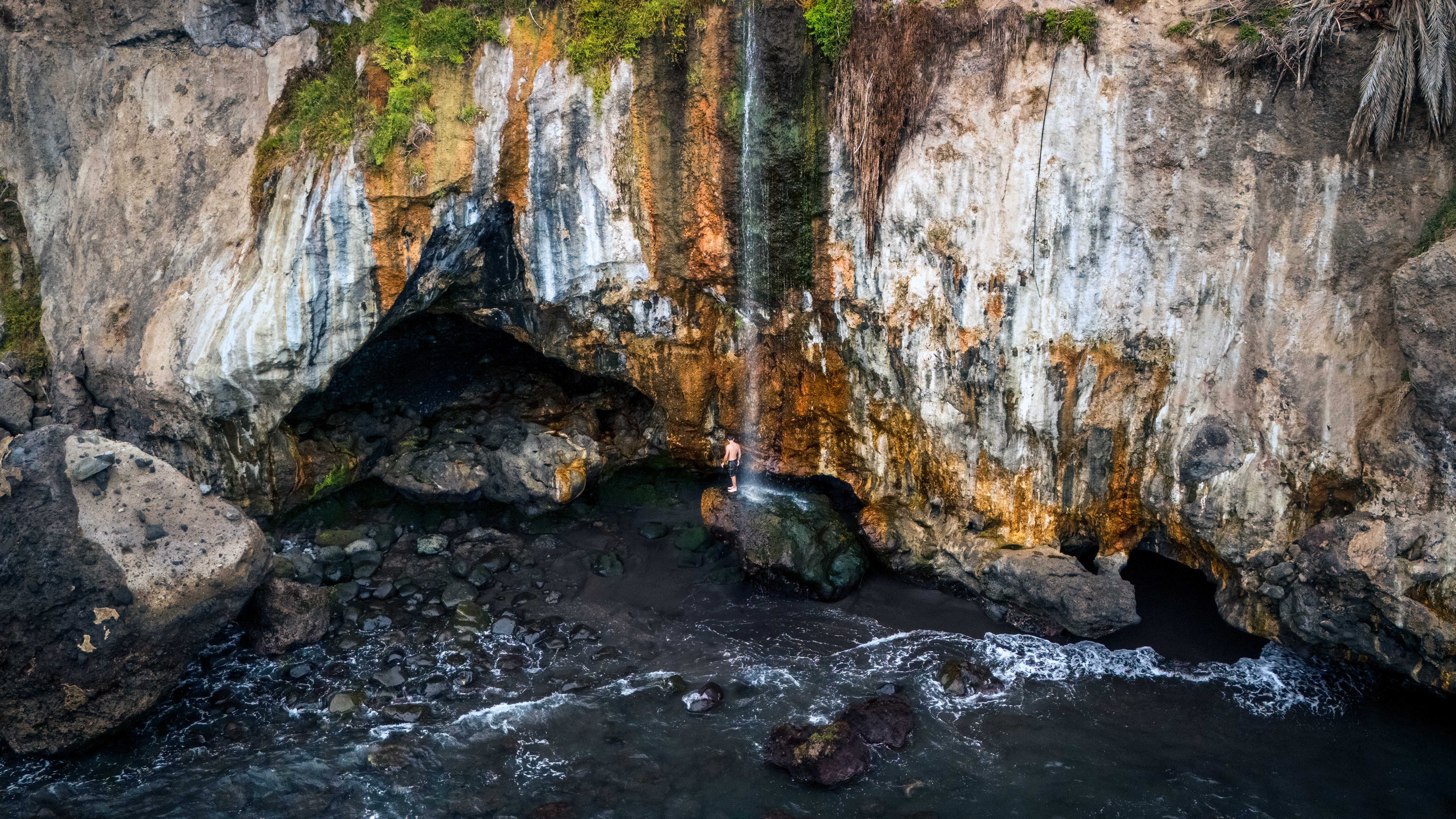 A waterfall is flowing into the ocean near a cliff · Free Stock Photo