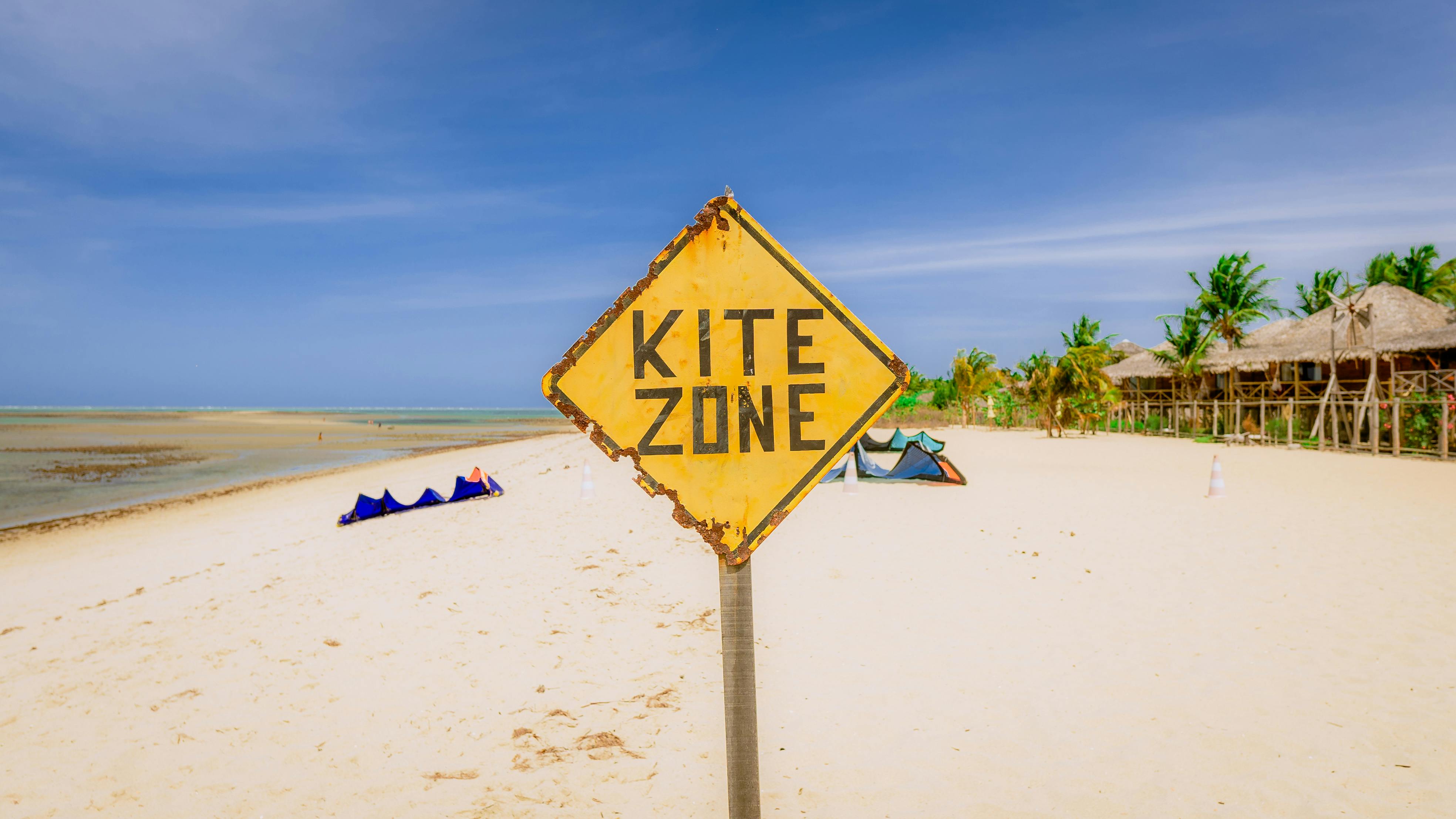 A yellow sign that says kite zone on the beach · Free Stock Photo