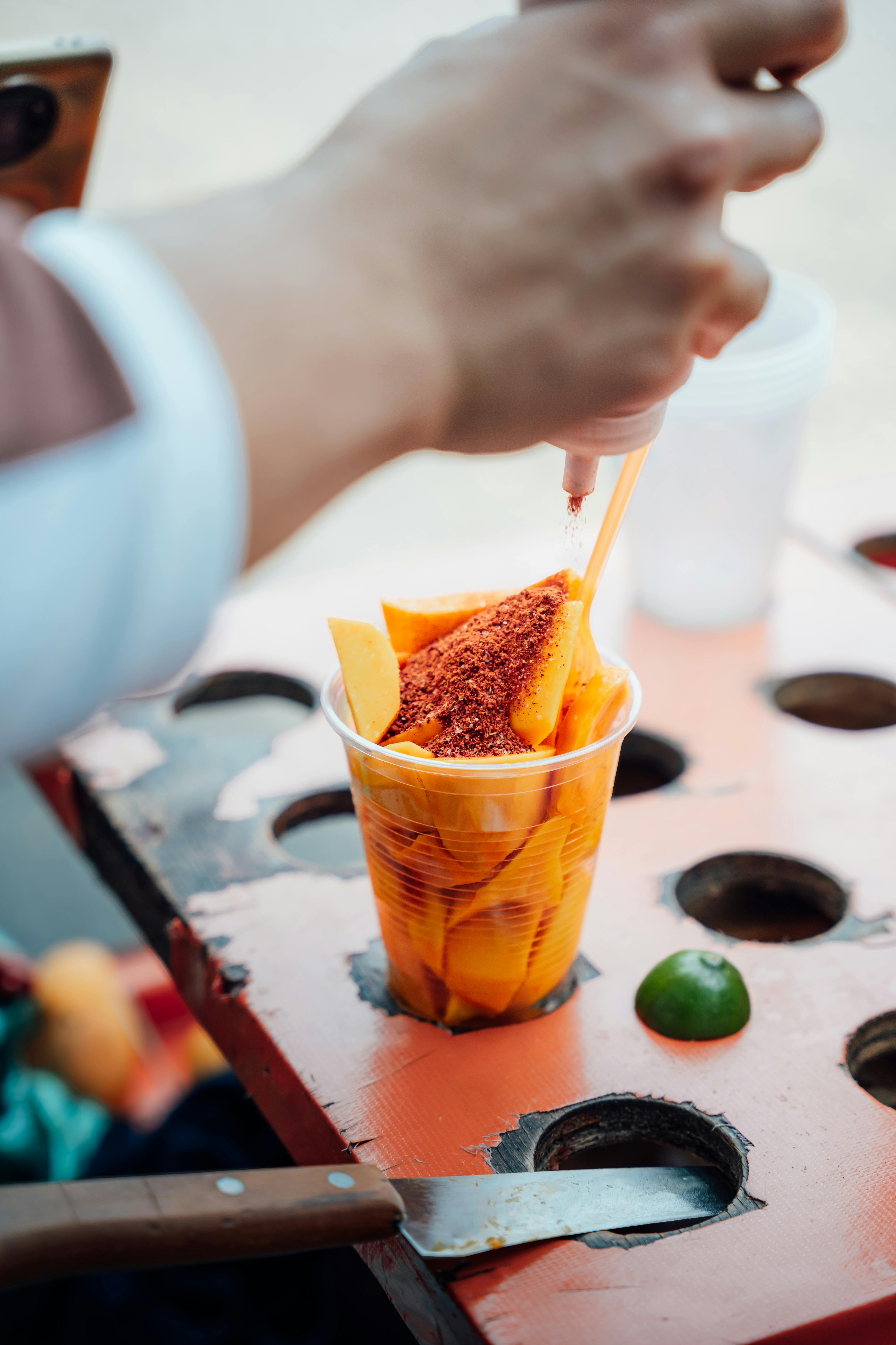 Hand Pouring Seasoning on Sliced Mango in a Cup · Free Stock Photo
