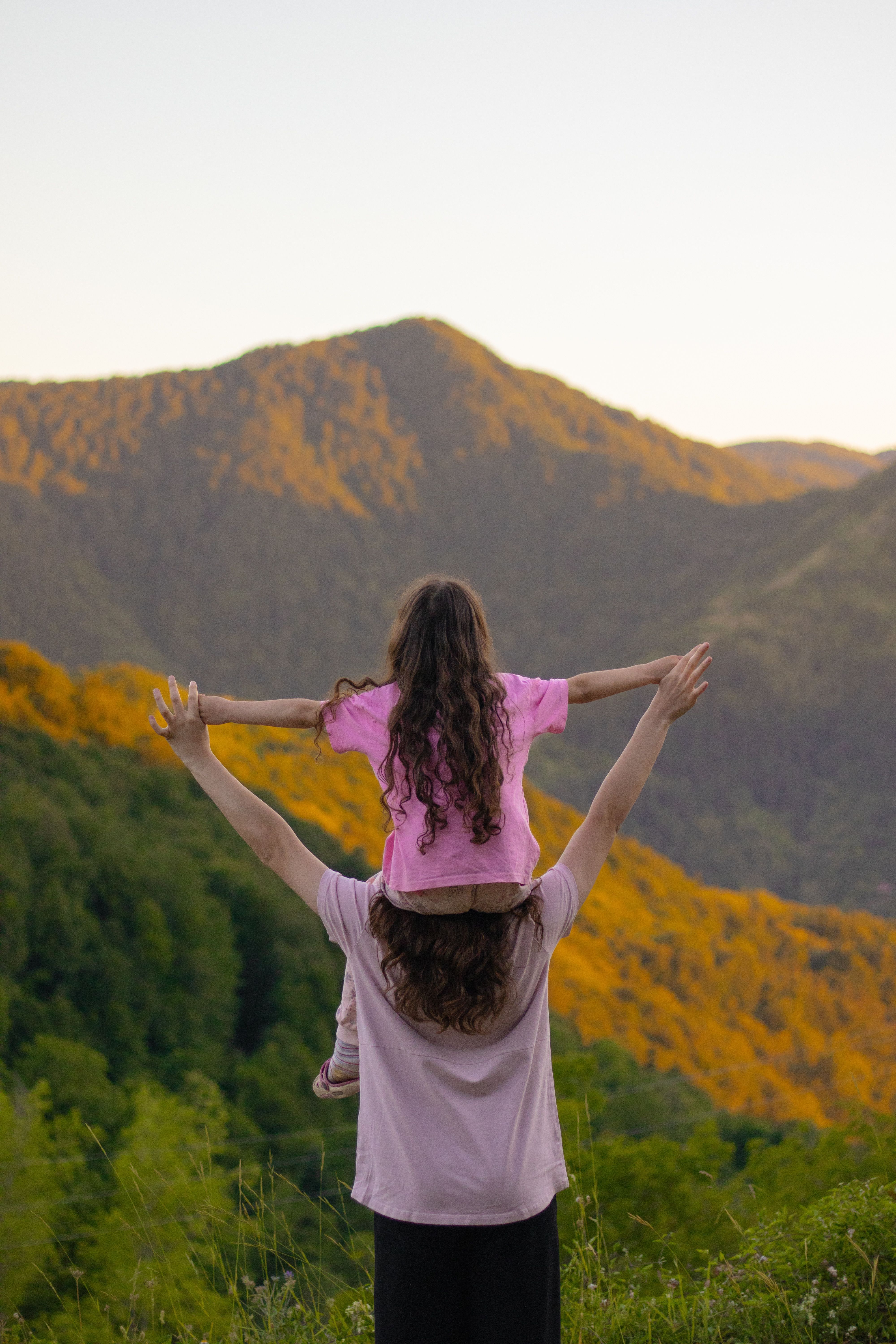 Back View Girl Sitting on a Womans Shoulders Looking at the Mountains ...