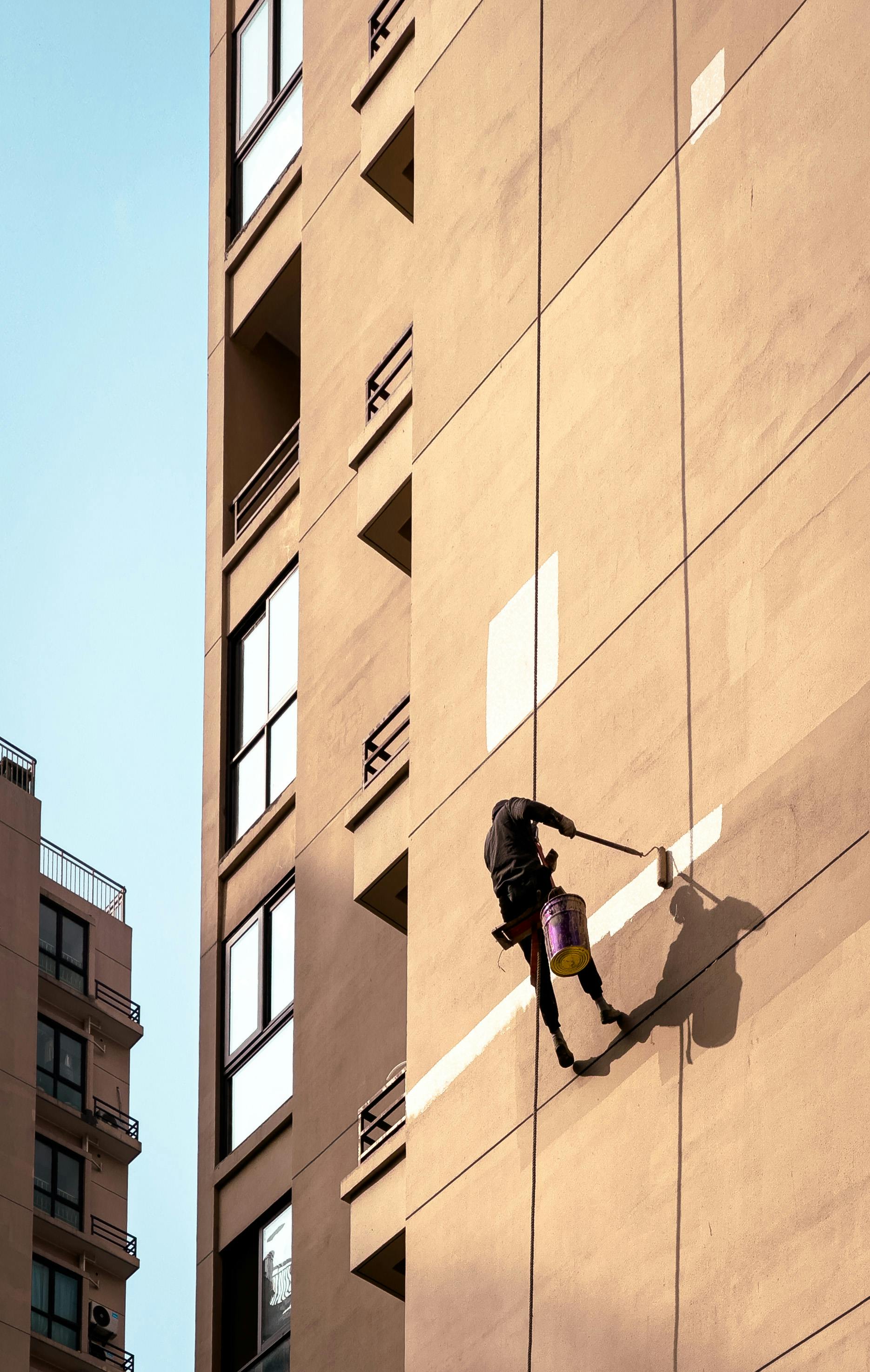 Two Construction Workers Painting A Building Facade Using Rope Access ...