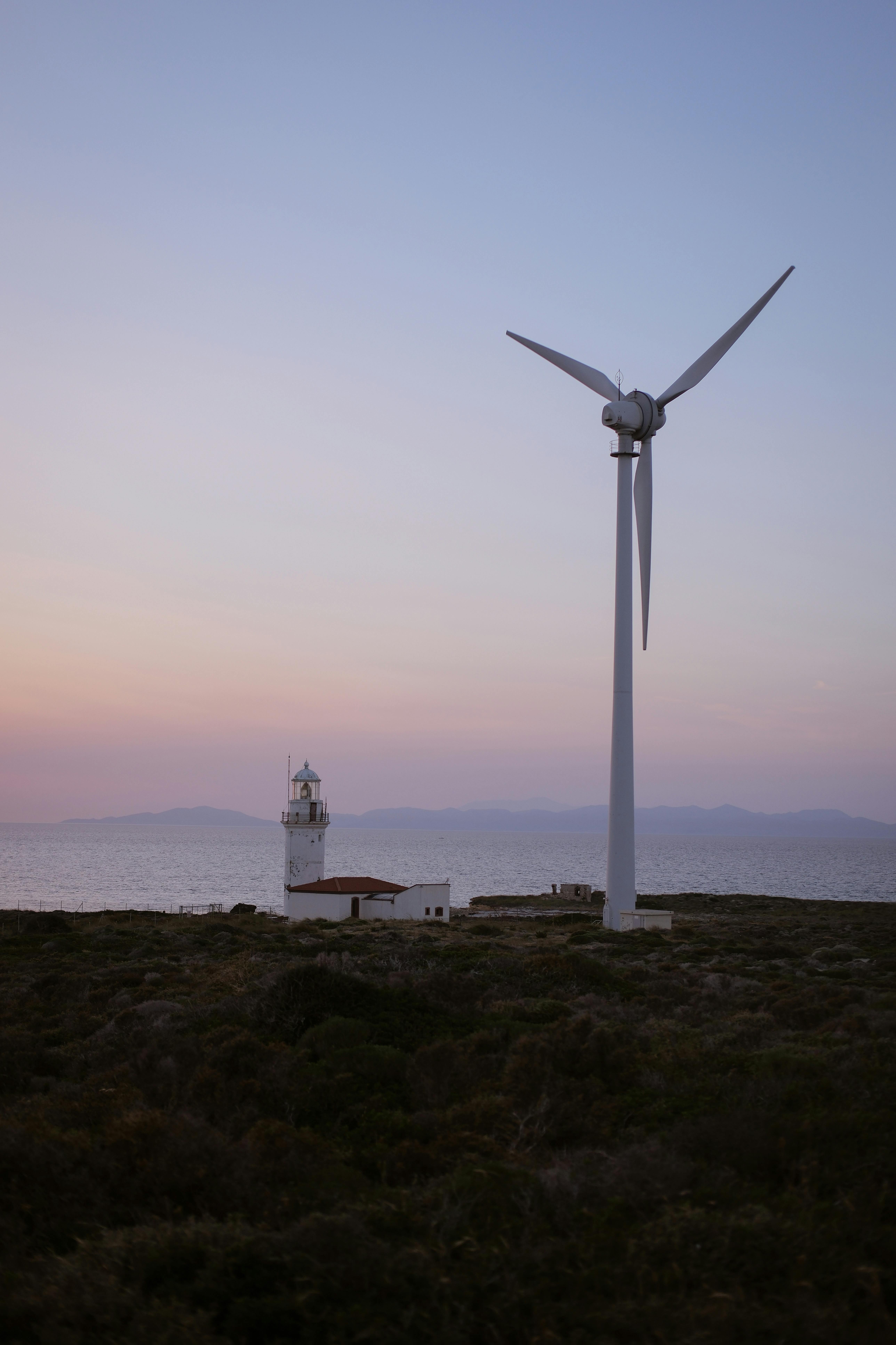 Wind Turbine behind a Coastal Lighthouse at Dusk · Free Stock Photo
