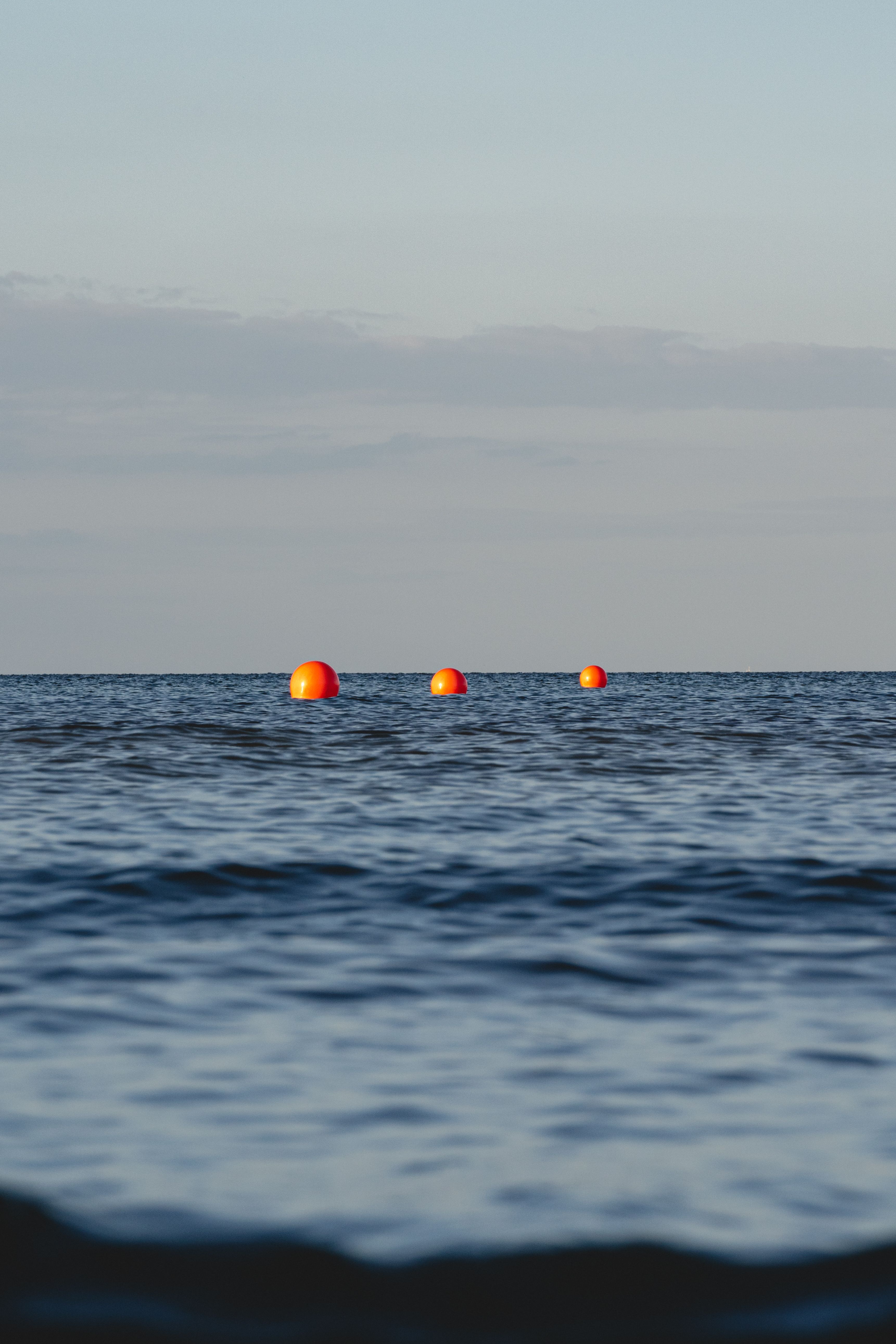 Three orange buoys floating in the ocean · Free Stock Photo