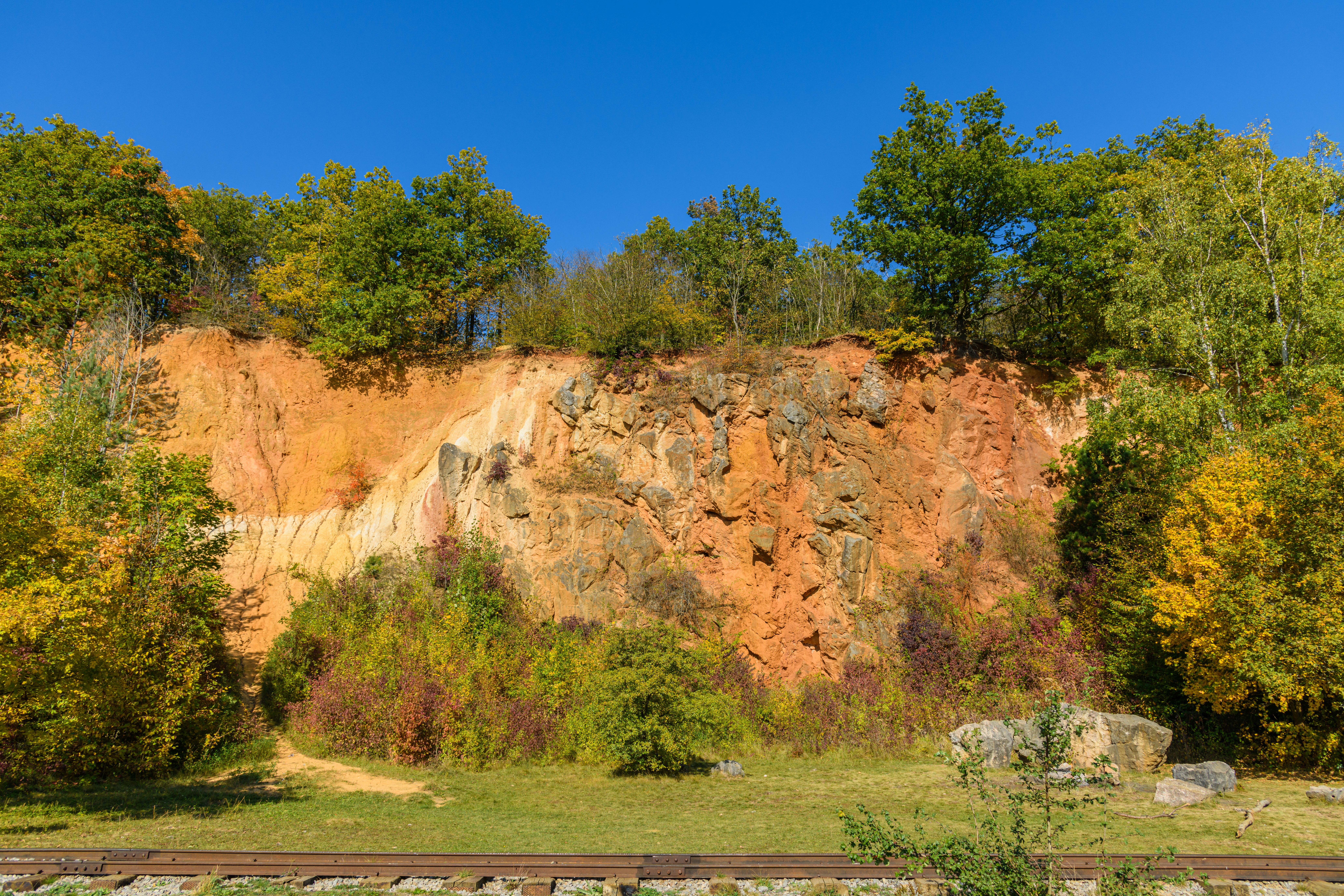 Sandstone Cliff Wall with Trees near Railway Tracks · Free Stock Photo