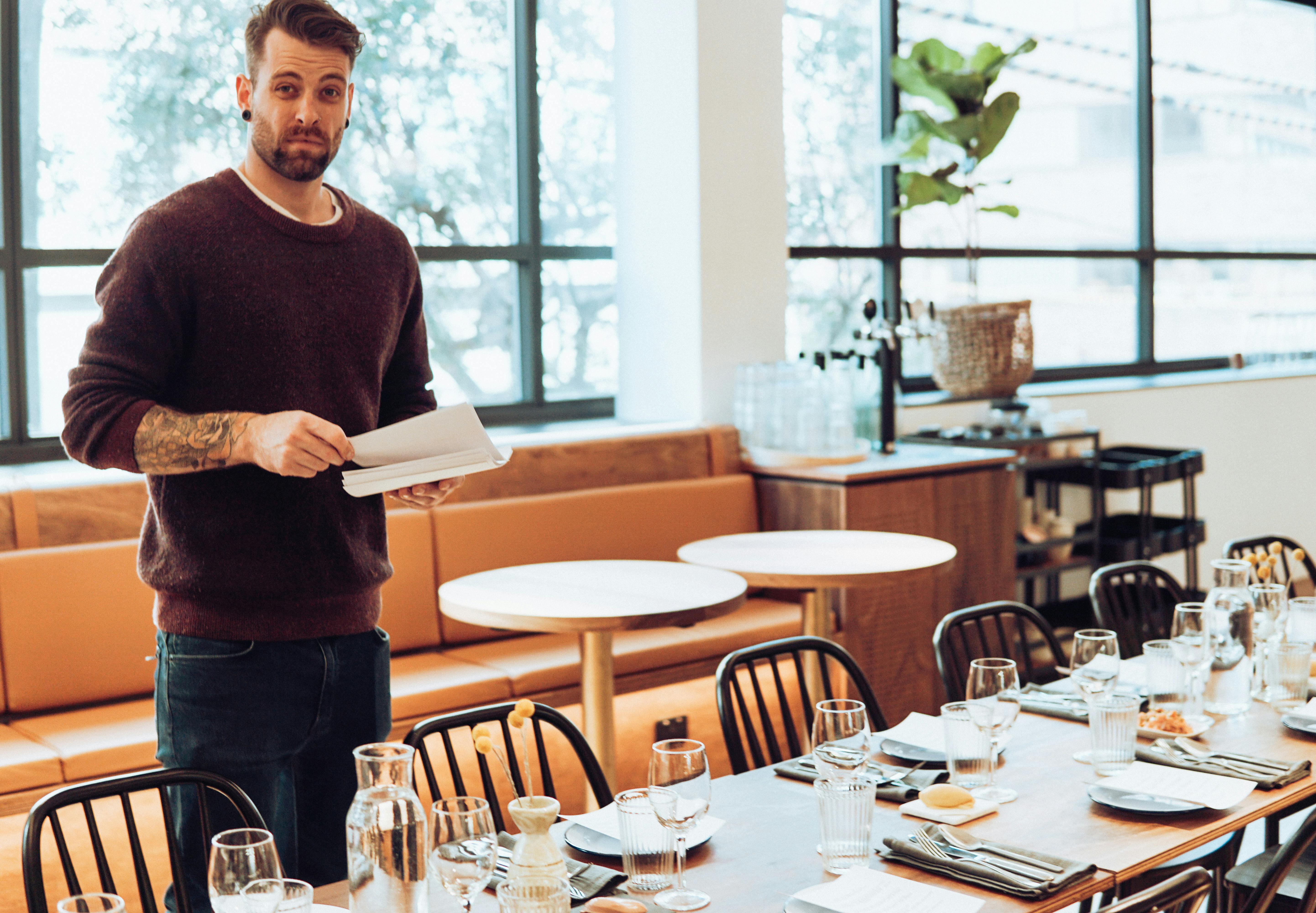 Man in Maroon Sweater Standing Beside Table Holding Book · Free Stock Photo