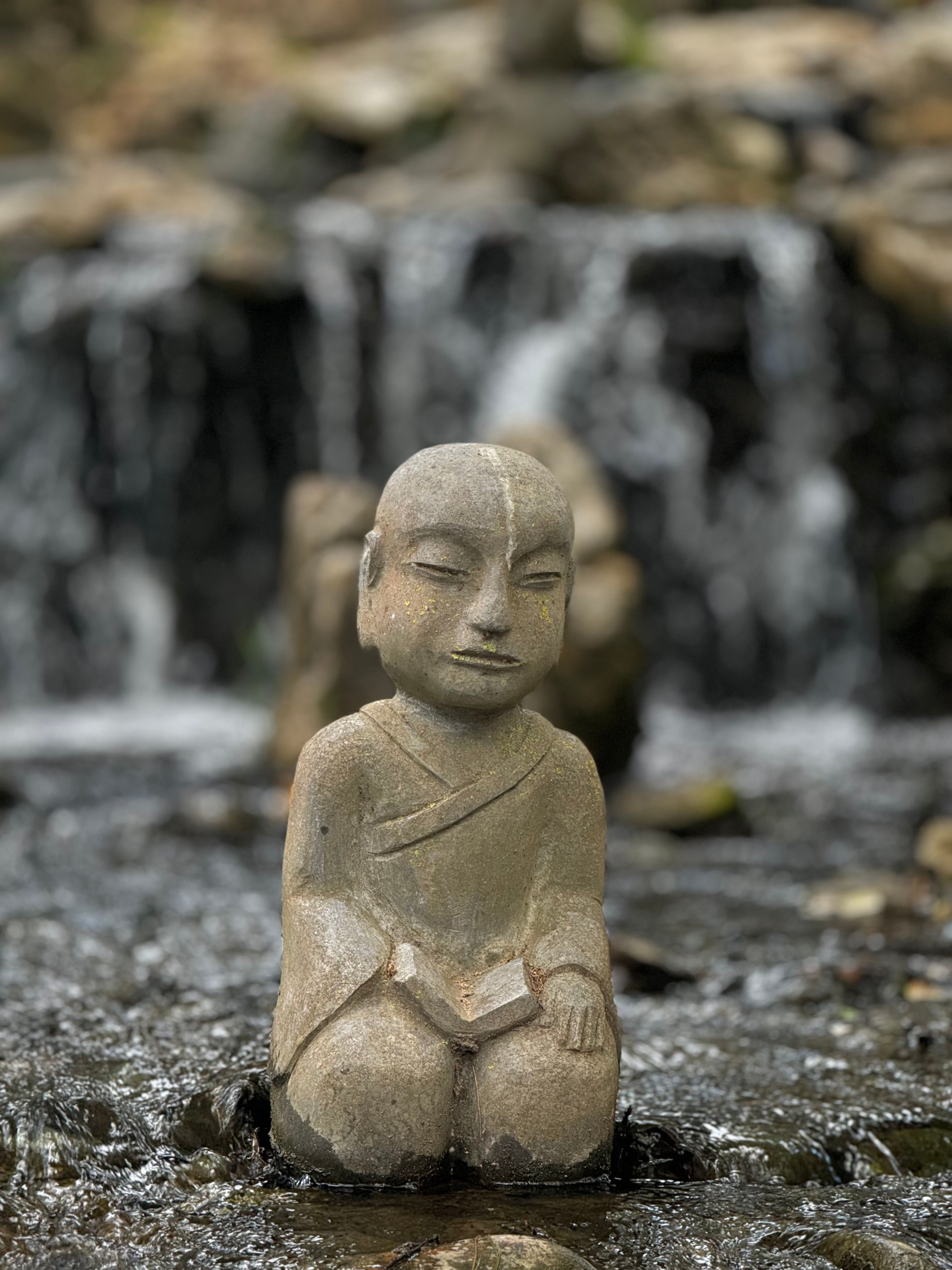 A stone statue of a buddha sitting in front of a waterfall · Free Stock ...