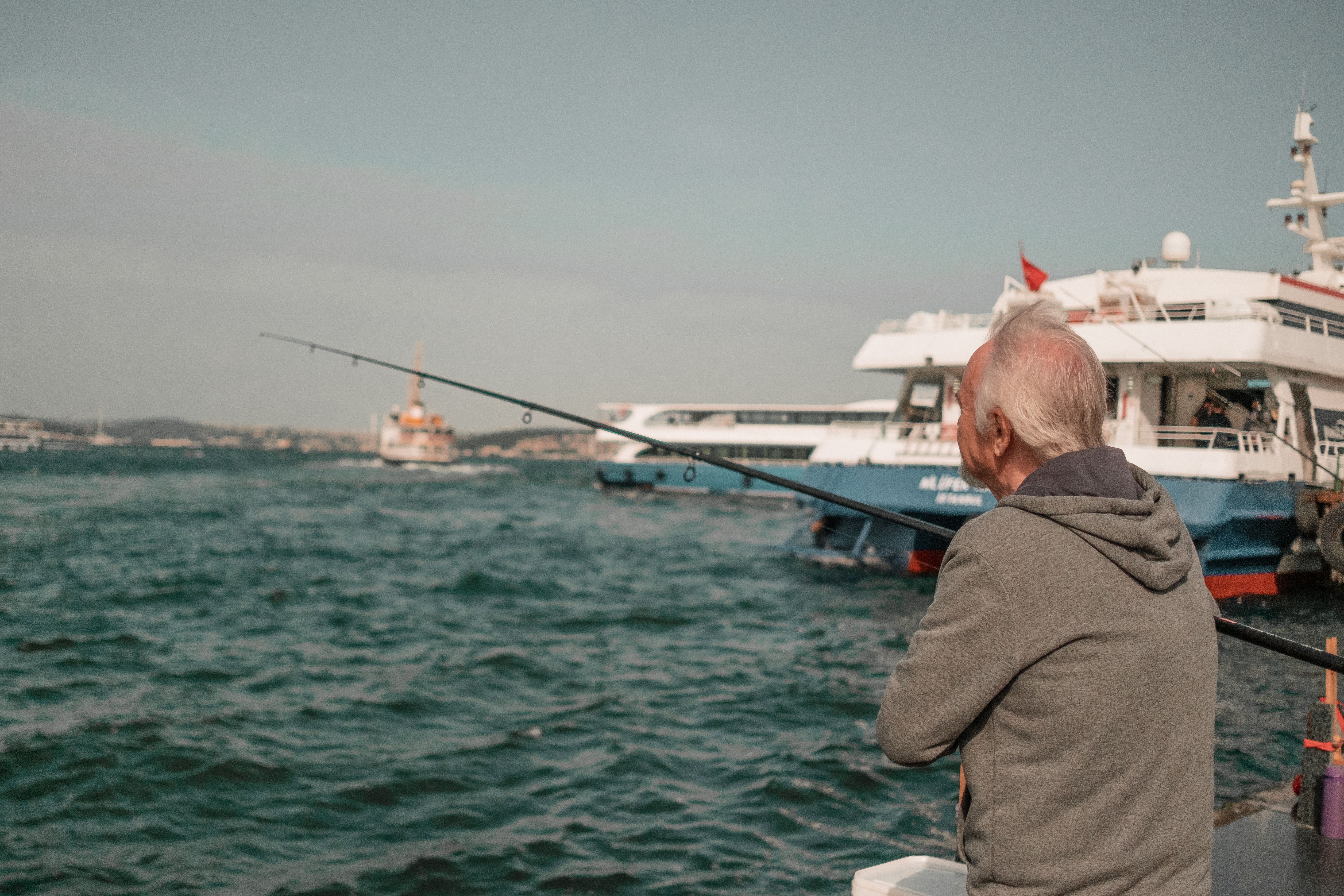 Angler Fishing on Shore with Ferries · Free Stock Photo