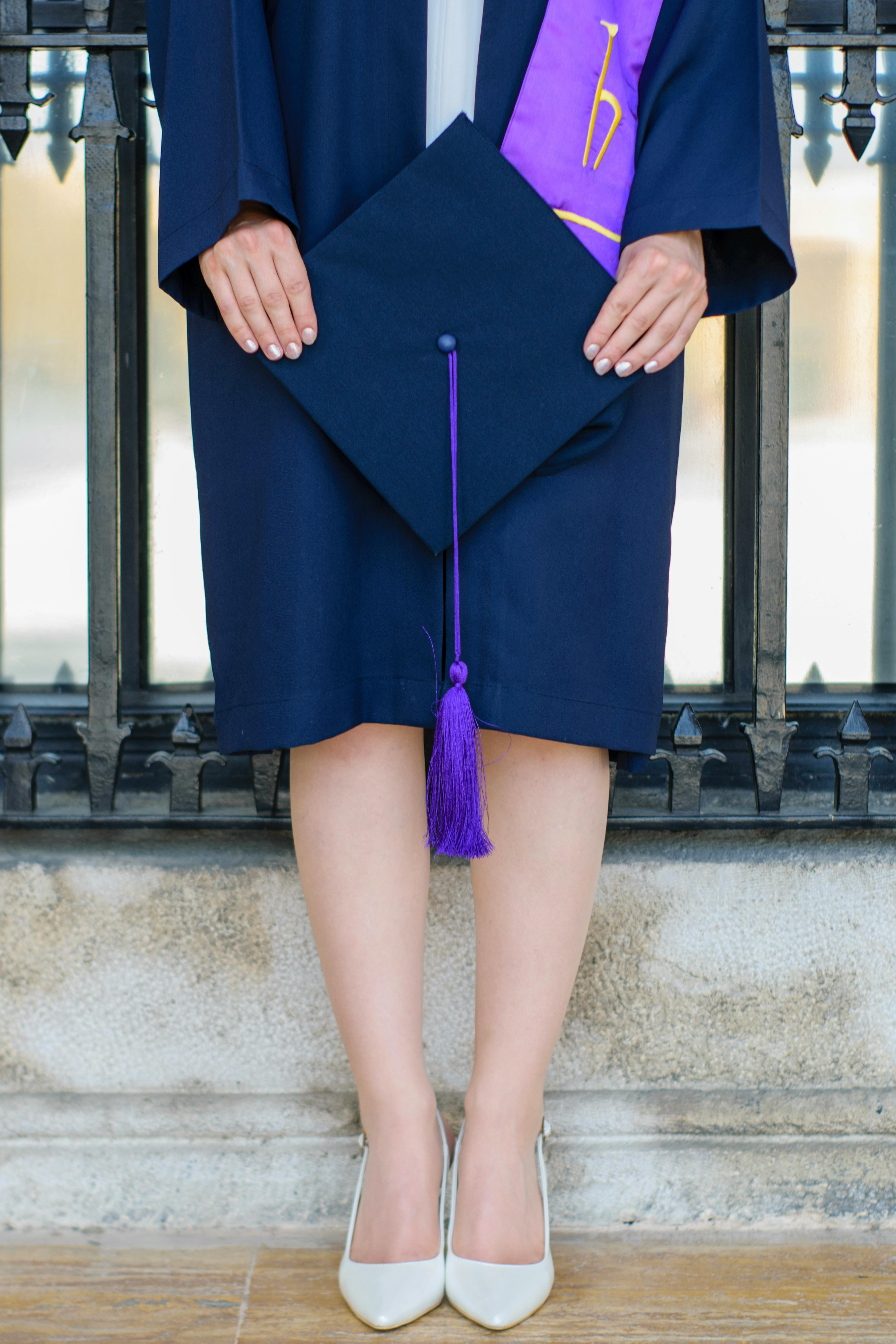 Legs of Woman Standing and Holding Academic Hat · Free Stock Photo