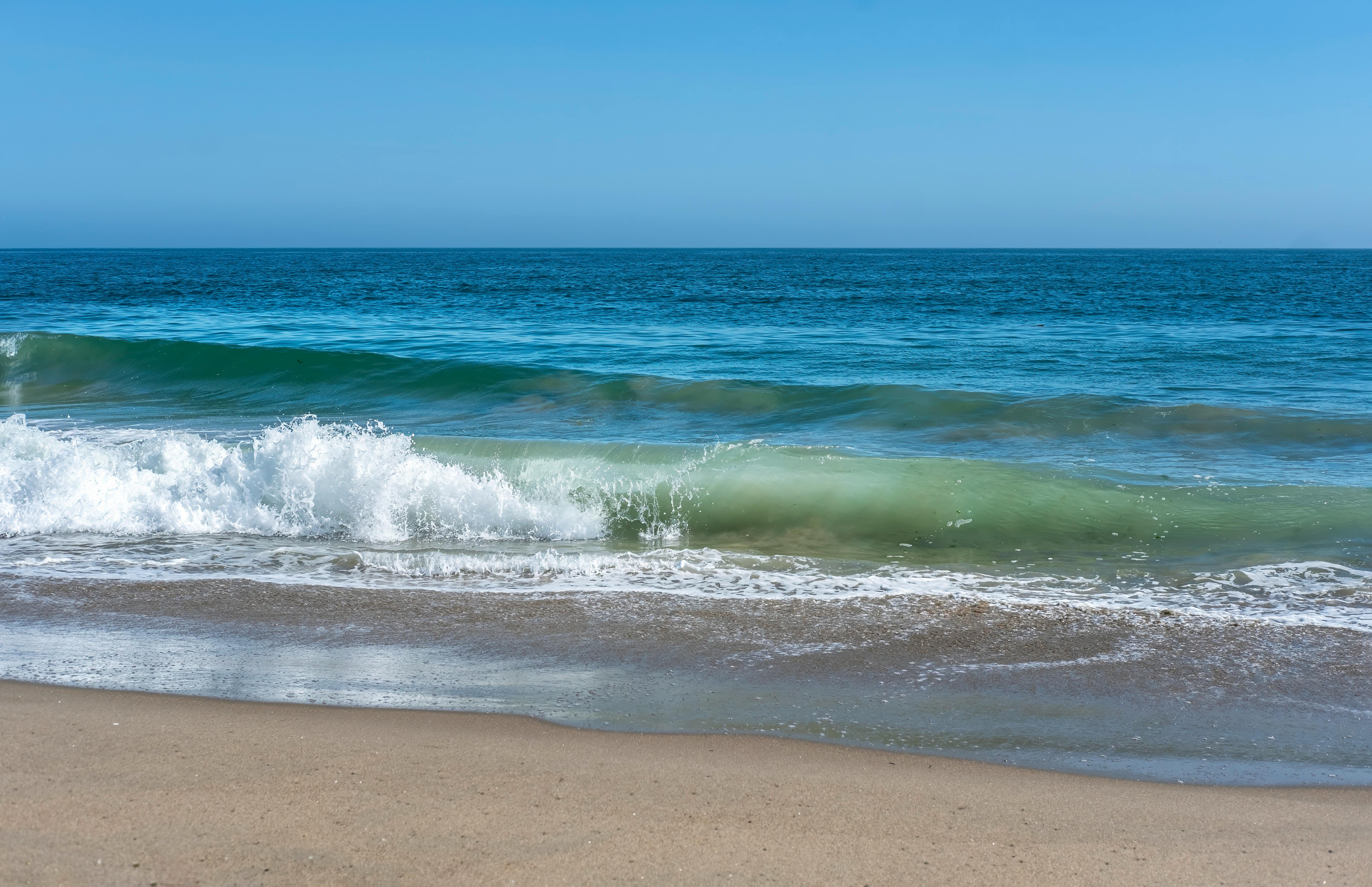 A beach with waves and sand on the shore · Free Stock Photo
