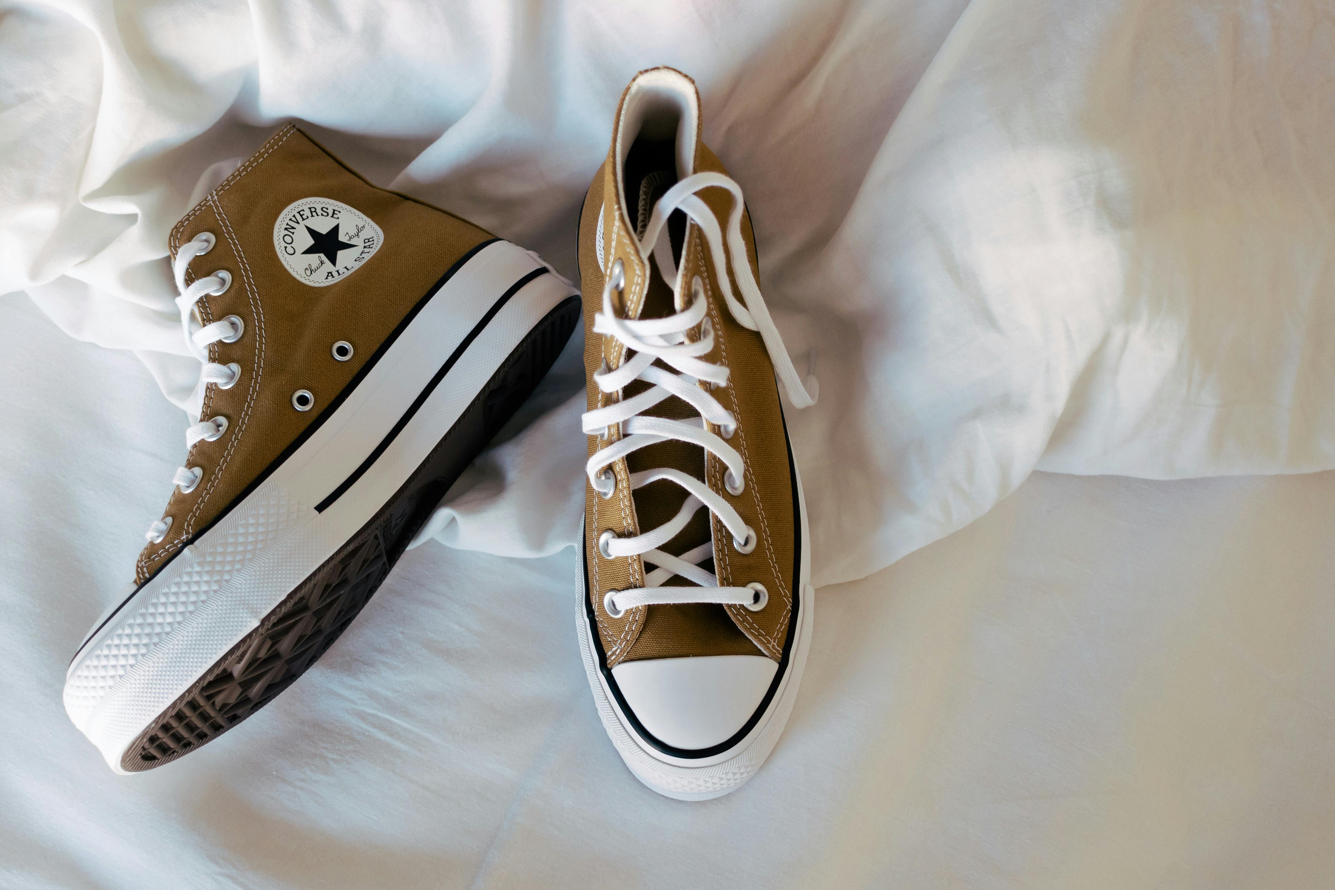 New Brown Converse Sneakers Lying on White Bed · Free Stock Photo