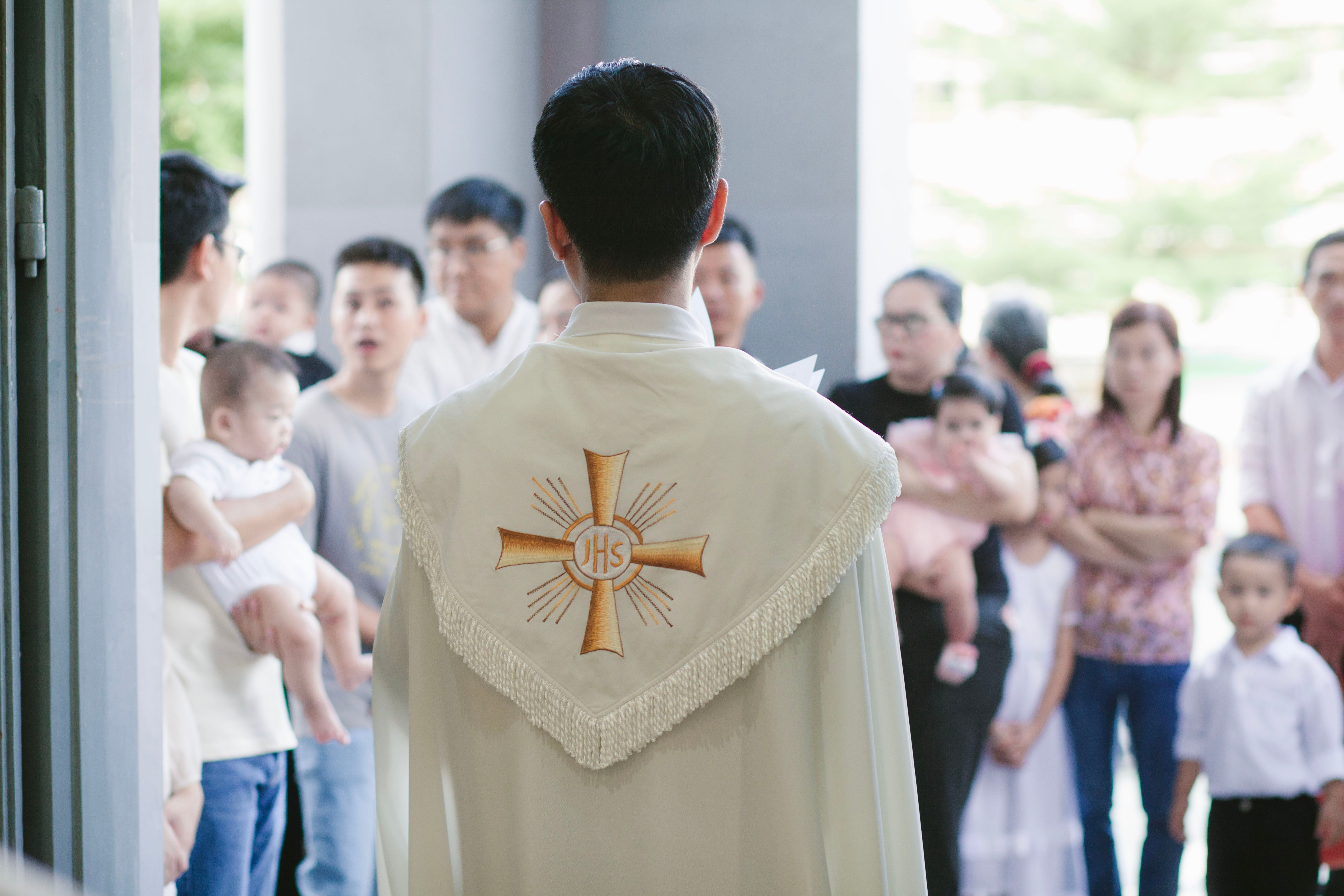 Back View of a Priest Standing in Front of People Holding Their Babies ...