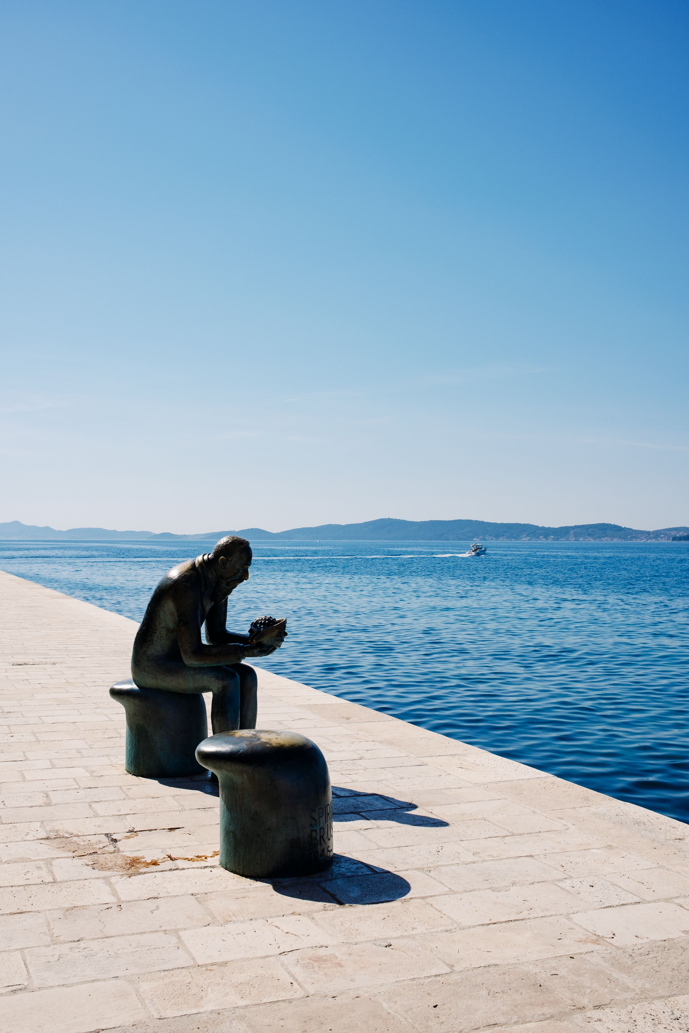 A statue of a man sitting on a bench by the water · Free Stock Photo