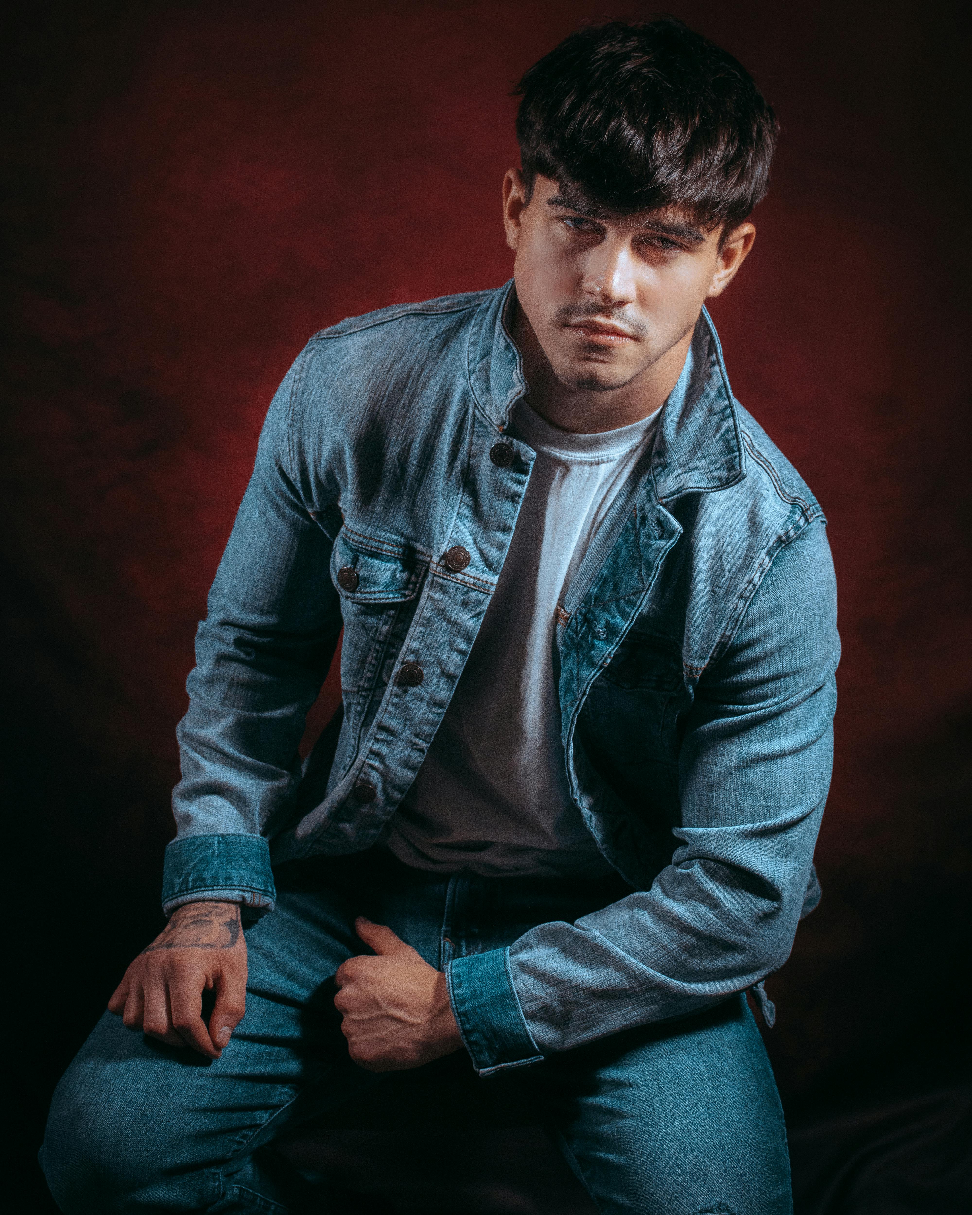 Man in Denim Jacket and Leans Leaning Elbow on Lap · Free Stock Photo