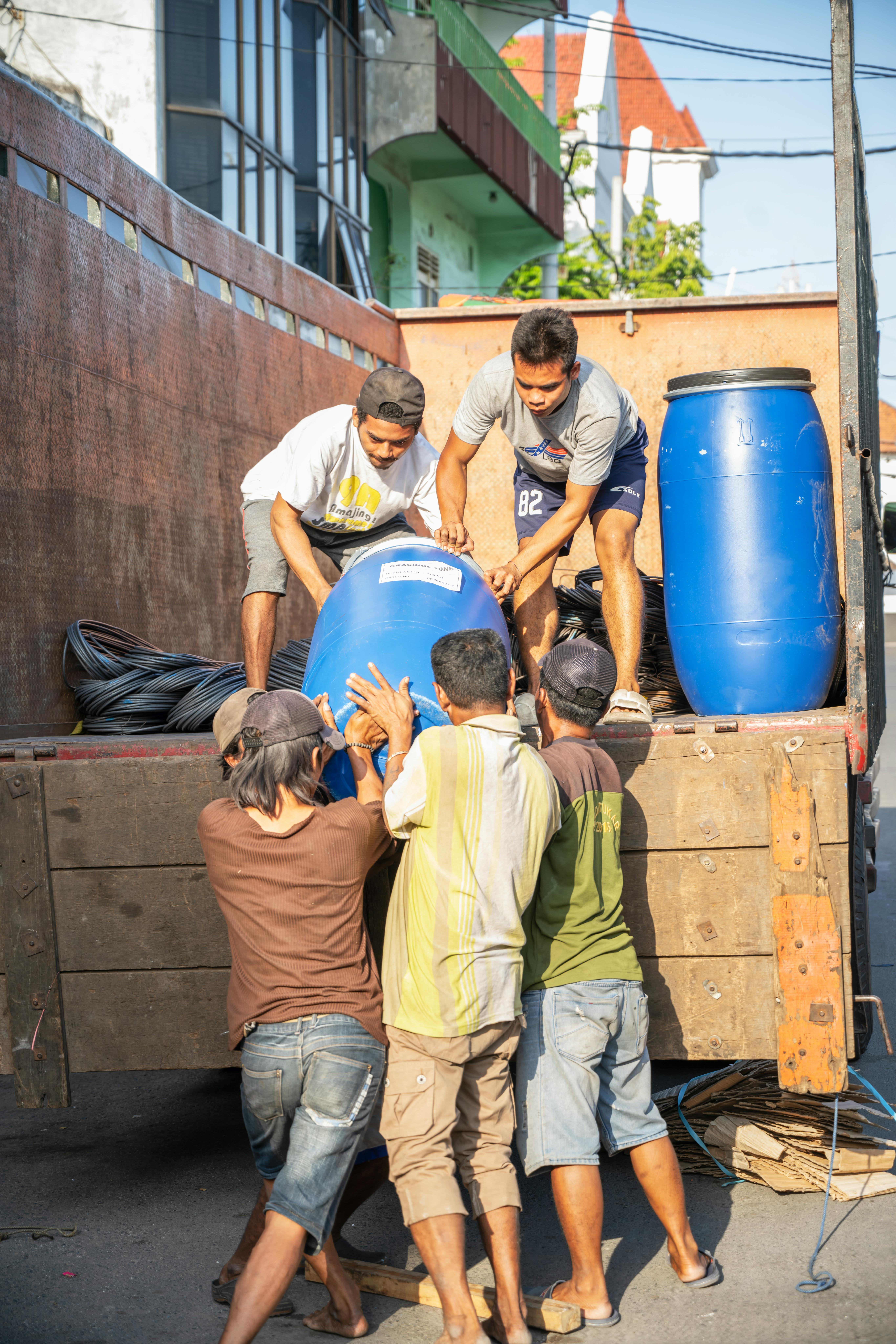 Men Loading Blue Barrels onto Large Truck · Free Stock Photo
