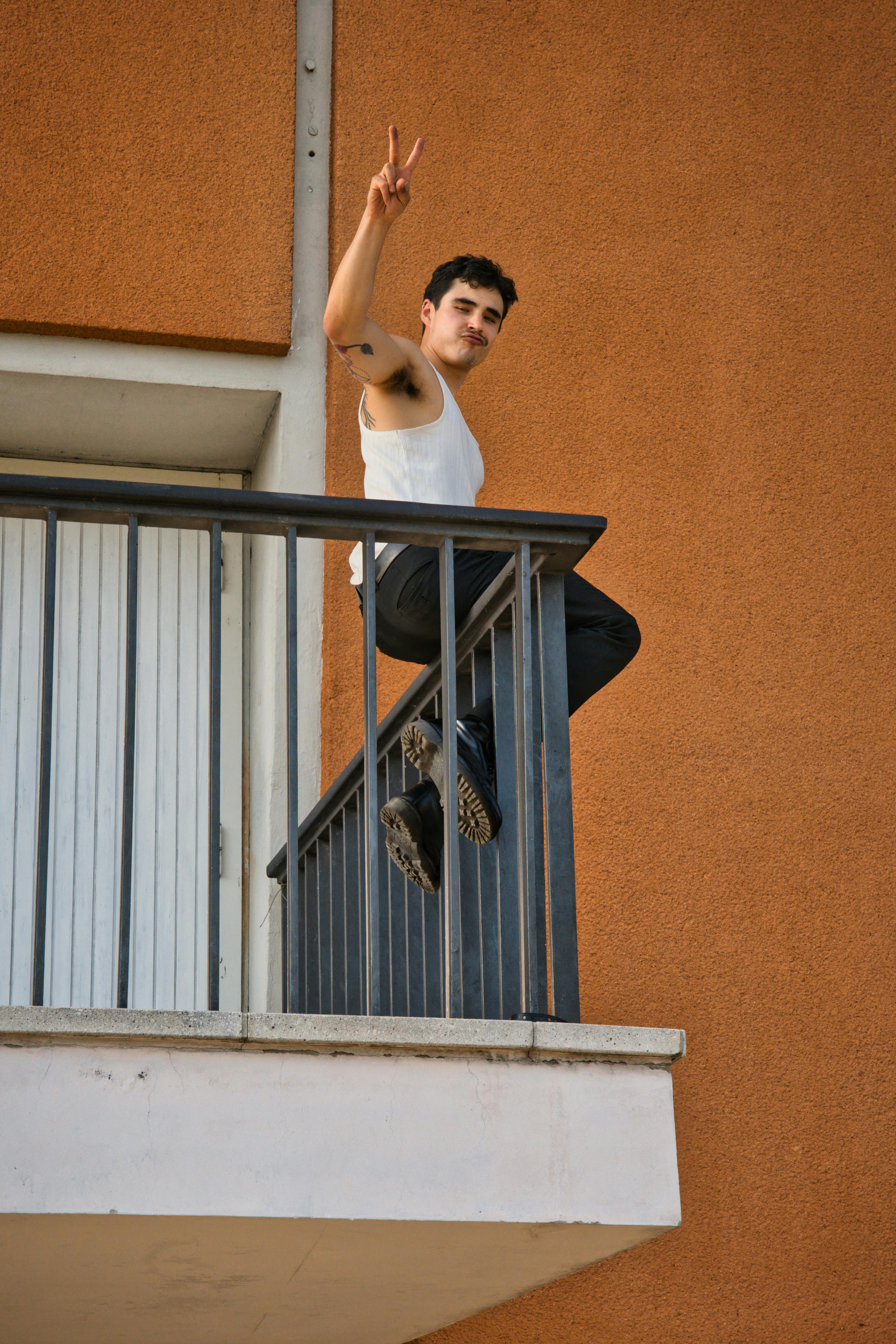 Man Sitting and Posing on Railing on Balcony · Free Stock Photo