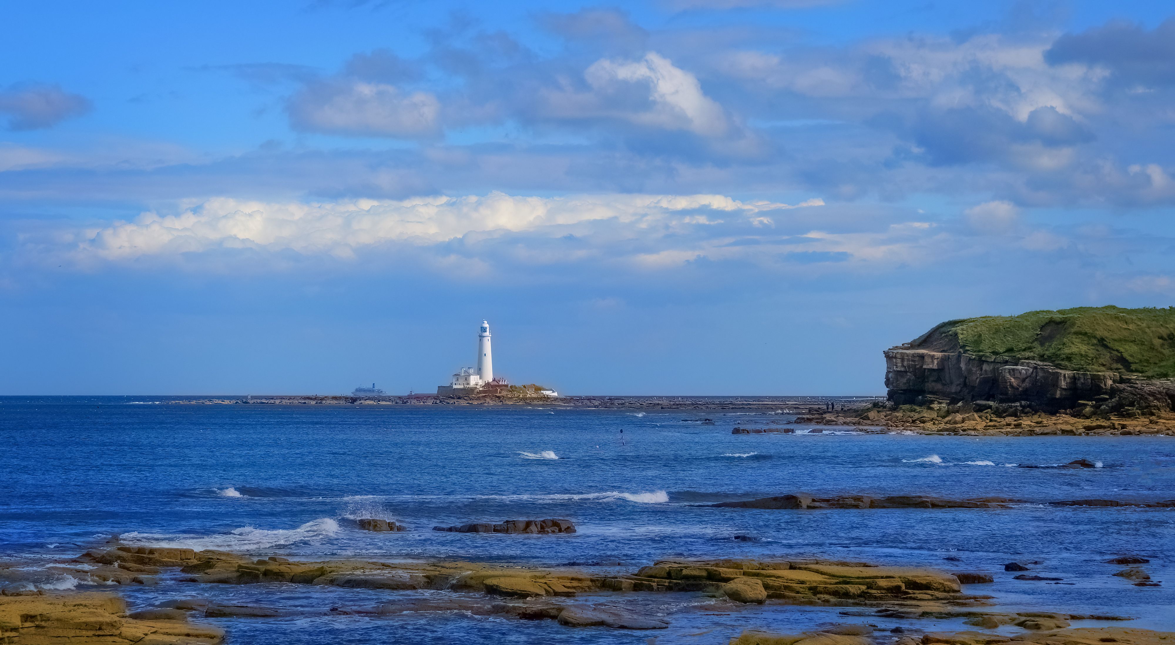 A lighthouse is seen in the distance on a rocky shore · Free Stock Photo
