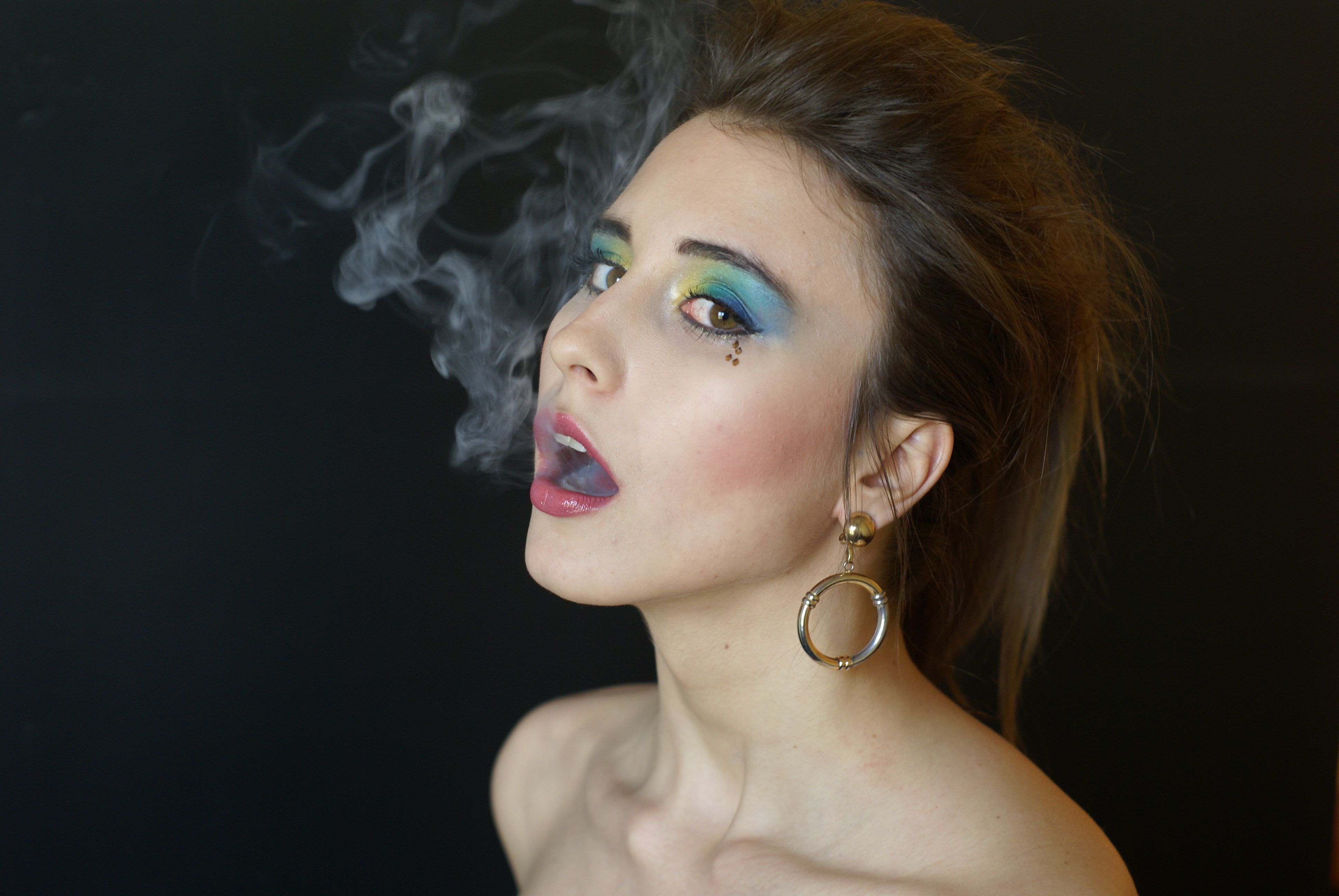 A woman with a colorful makeup and smoke in her mouth · Free Stock Photo