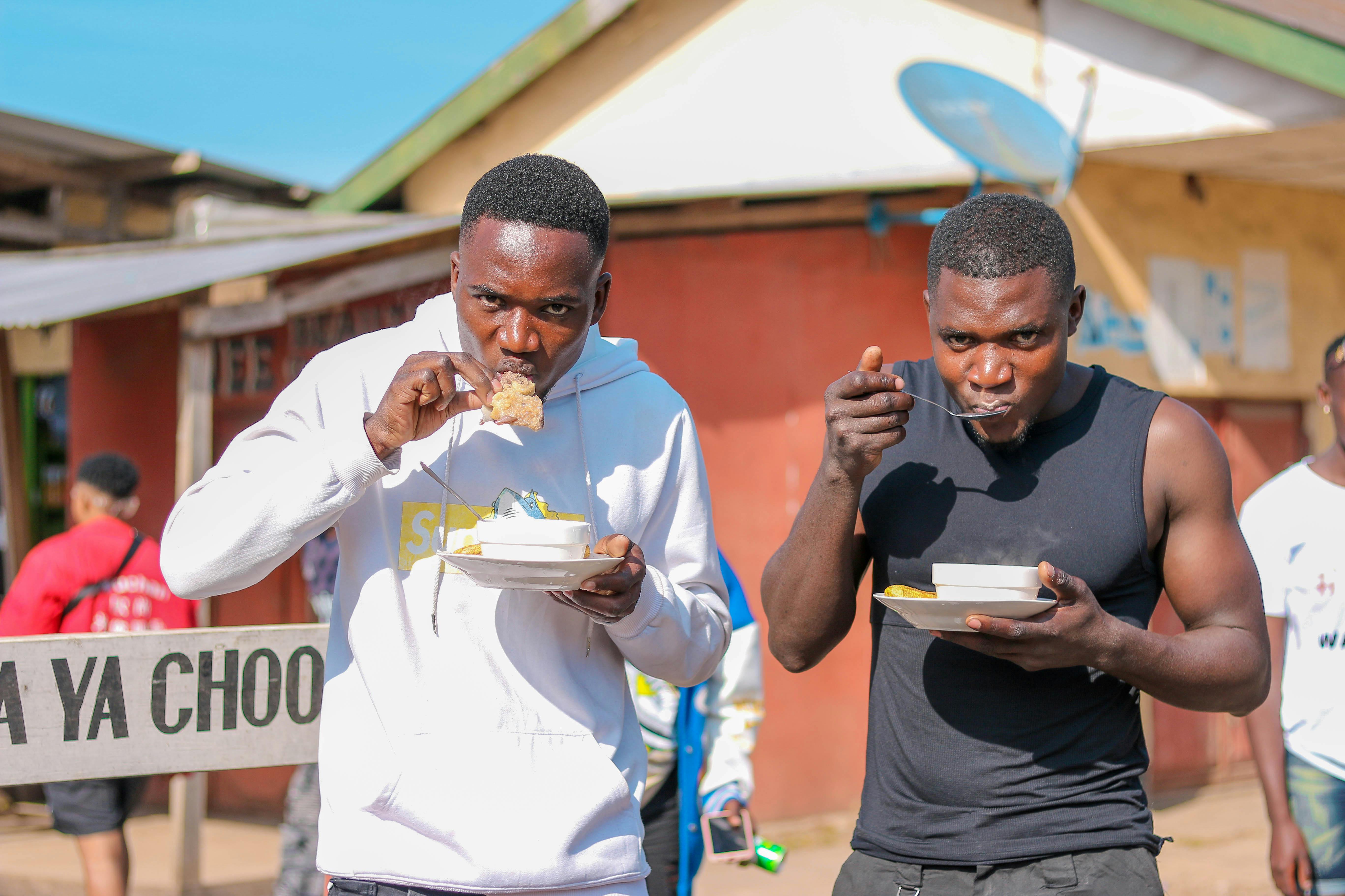 Two men eating food in front of a building · Free Stock Photo