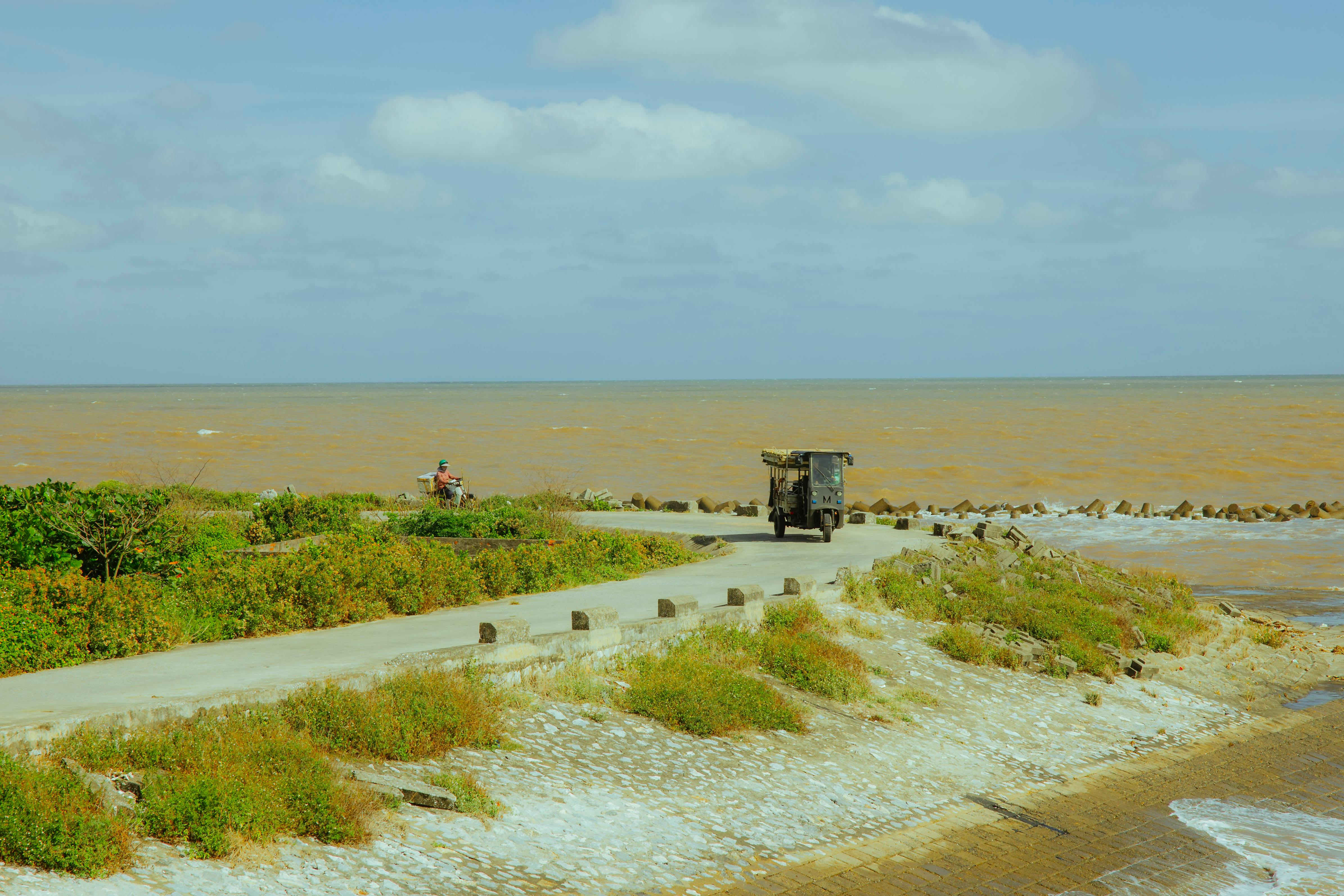 Serene Coastal Road with Rustic Vehicle and Vast Sea · Free Stock Photo
