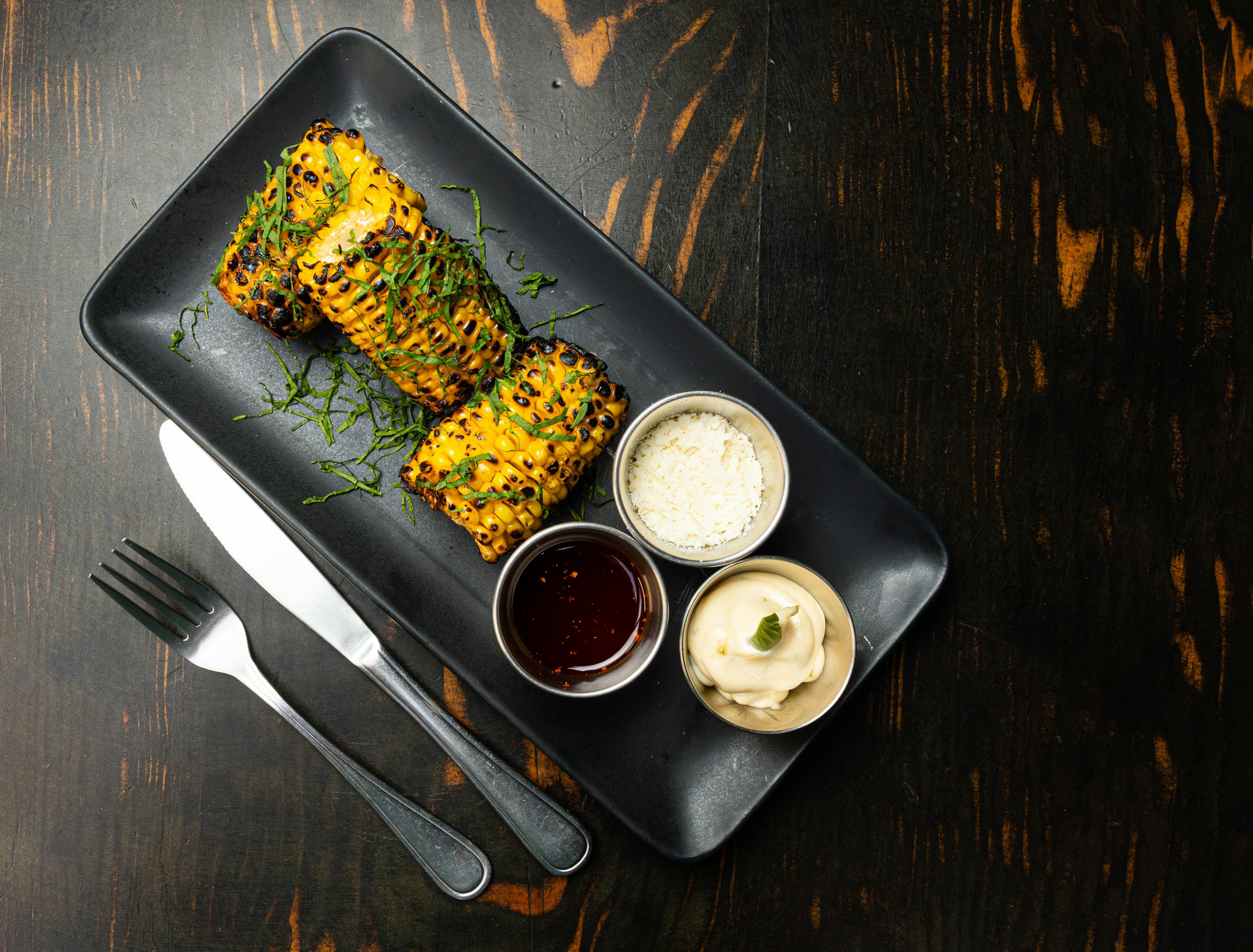 Grilled corn with a side of sauce and dipping sauce · Free Stock Photo