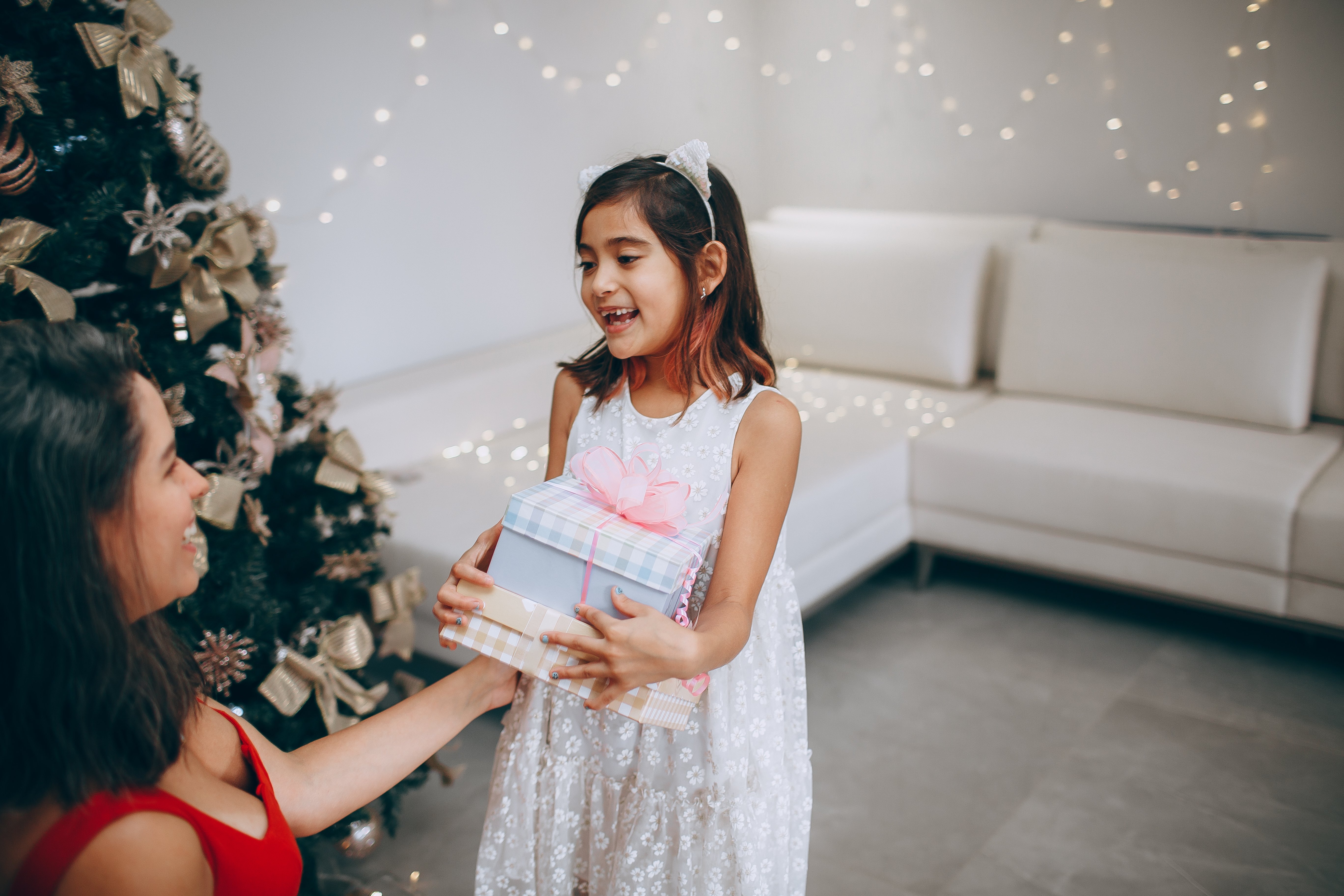 A woman giving a girl a gift near a christmas tree · Free Stock Photo