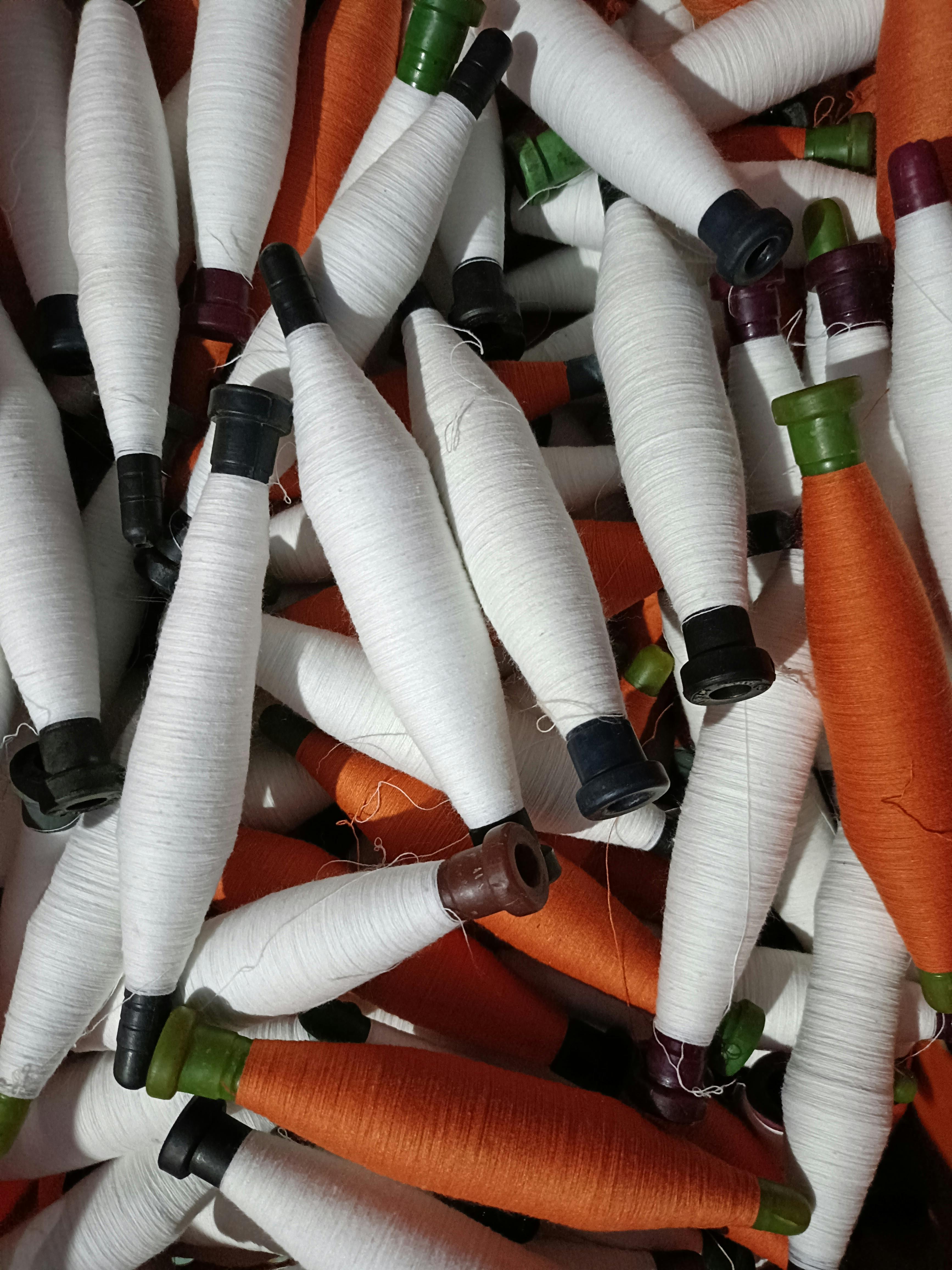 A pile of spools of thread with orange and white ones · Free Stock Photo