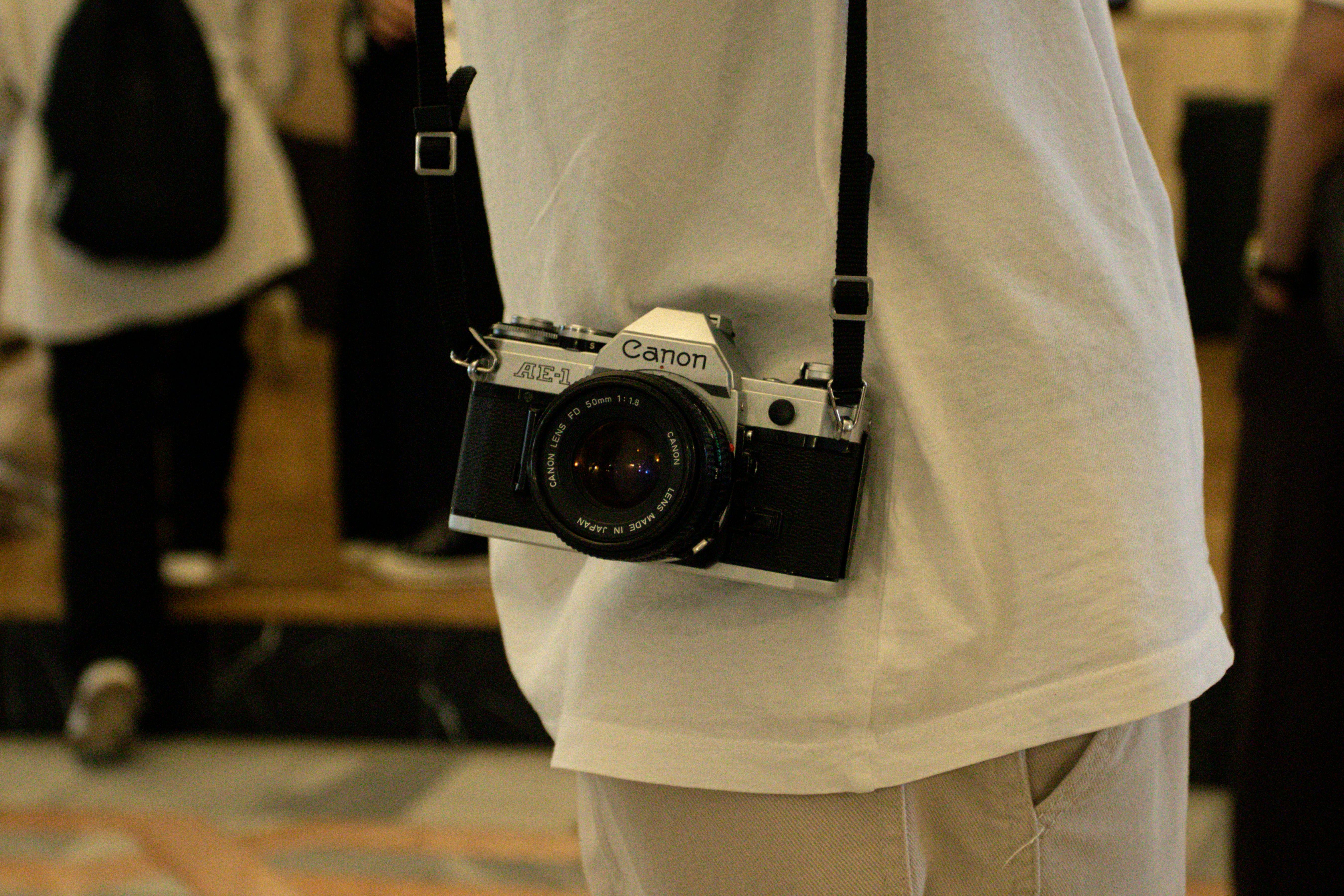 A person holding a camera with a strap around his neck · Free Stock Photo
