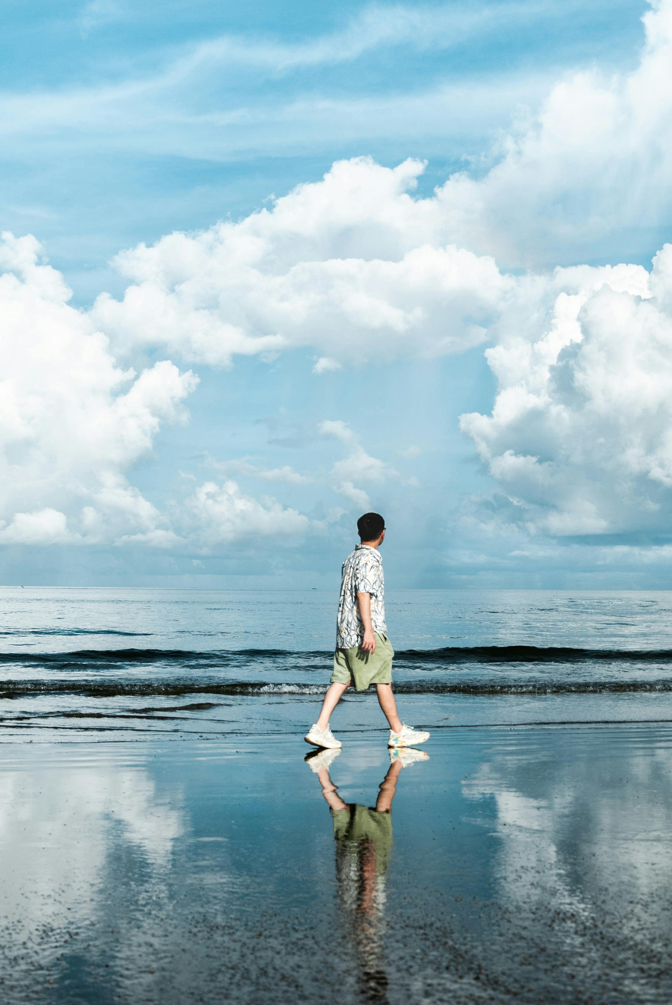 A man walking on the beach with clouds in the sky · Free Stock Photo