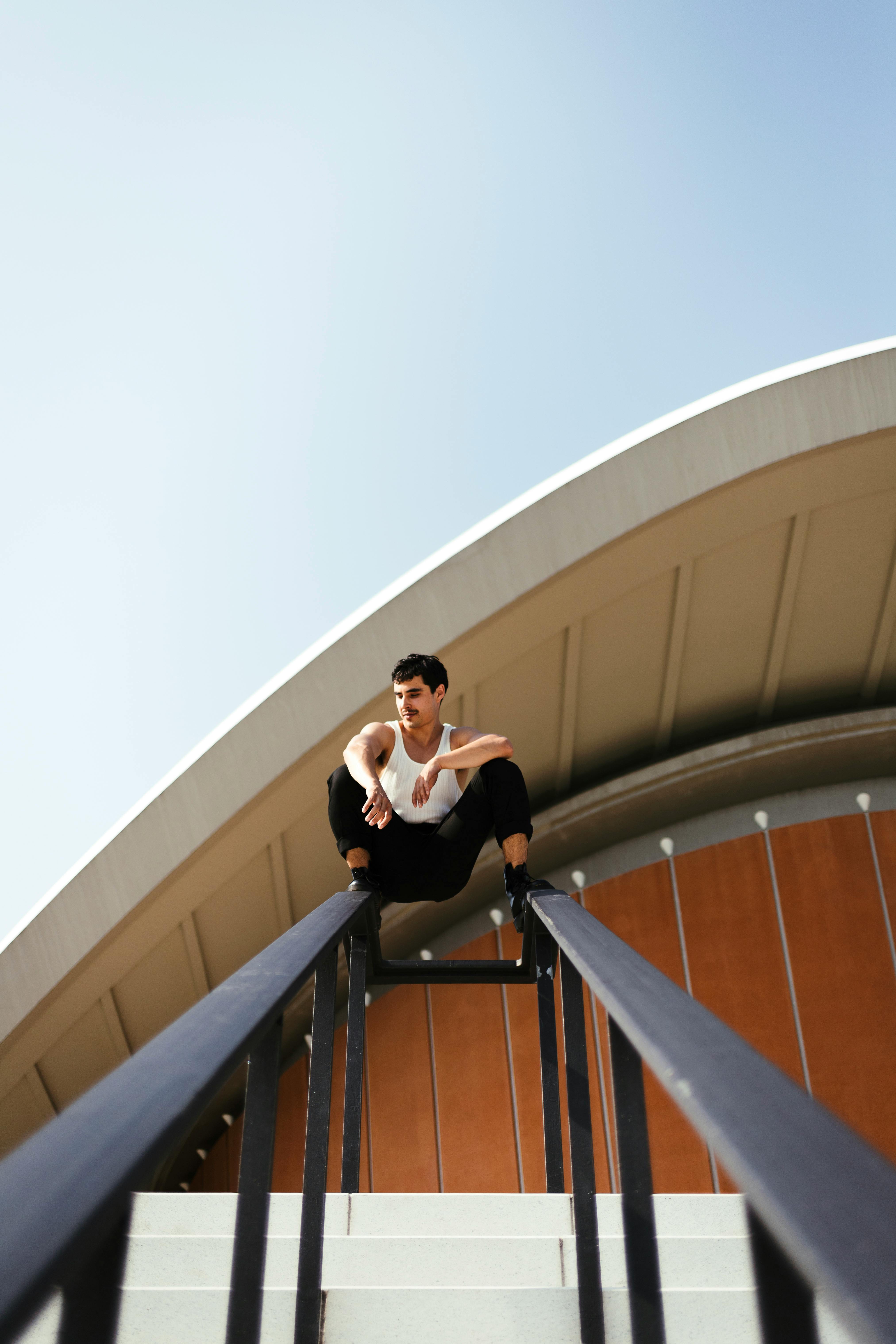 Low Angle Shot of a Man Sitting on a Rail · Free Stock Photo