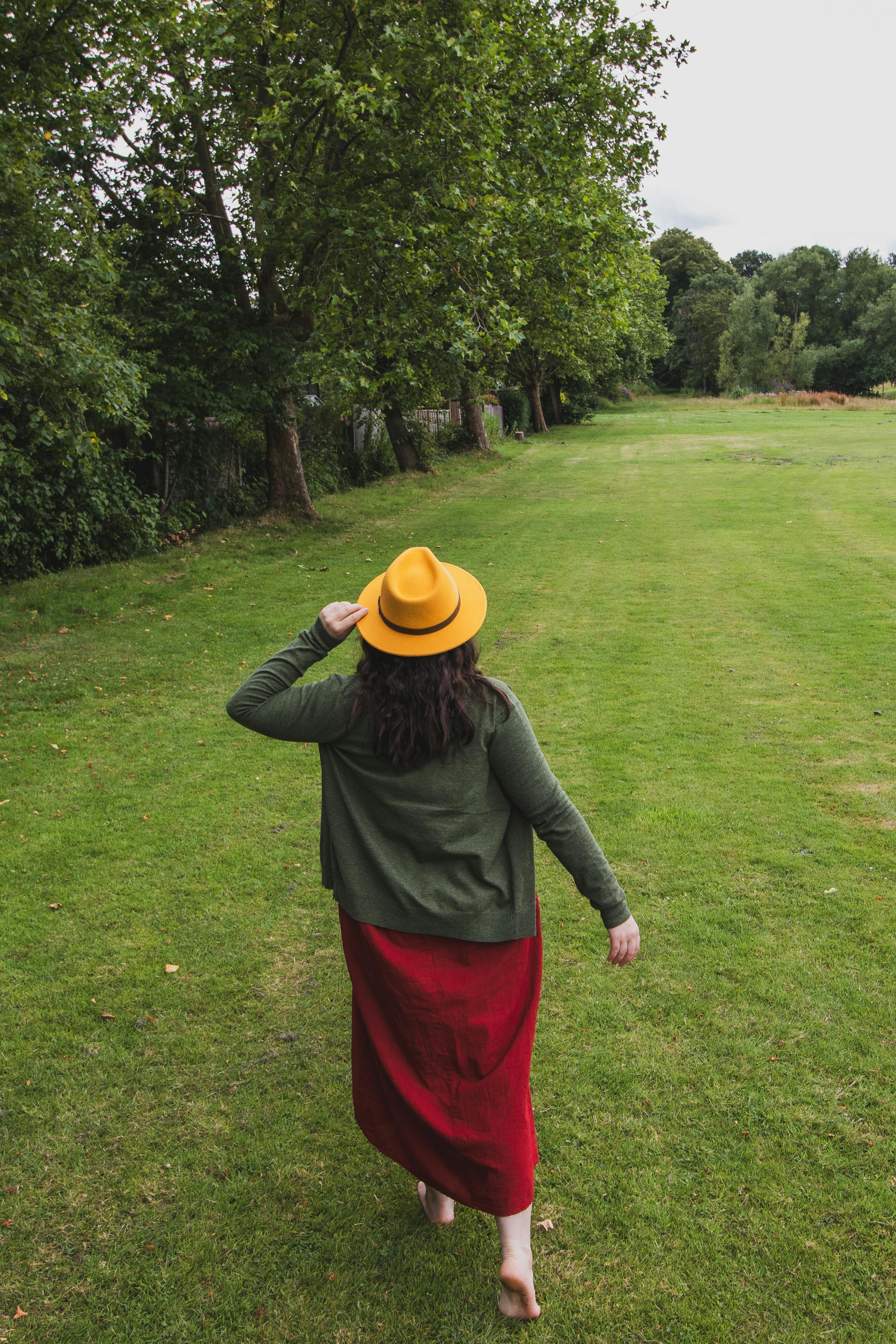 Back View of Woman in Yellow Hat and Red Skirt Walking Barefoot on ...
