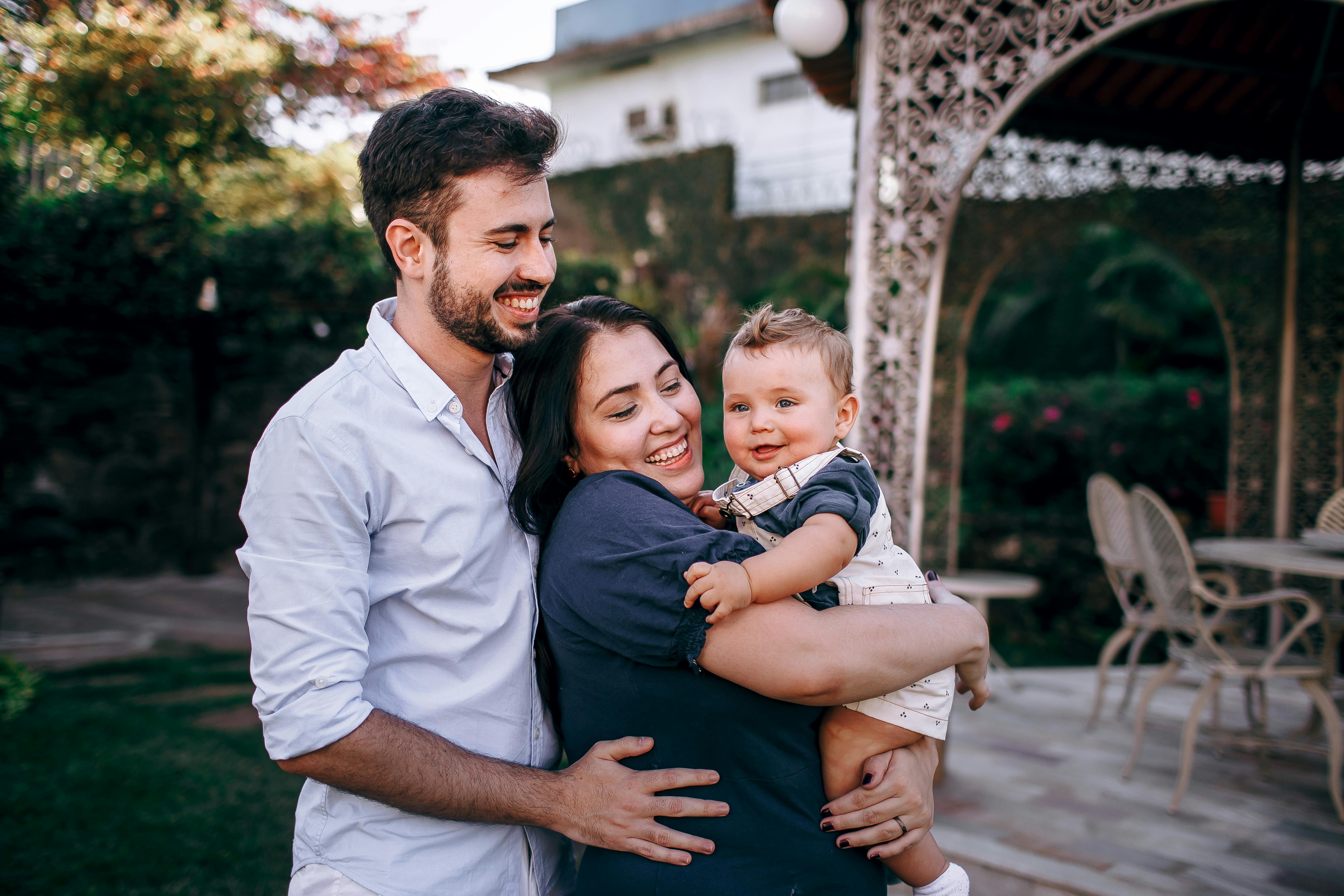 Smiling Parents Hugging Holding Their Infant Baby · Free Stock Photo