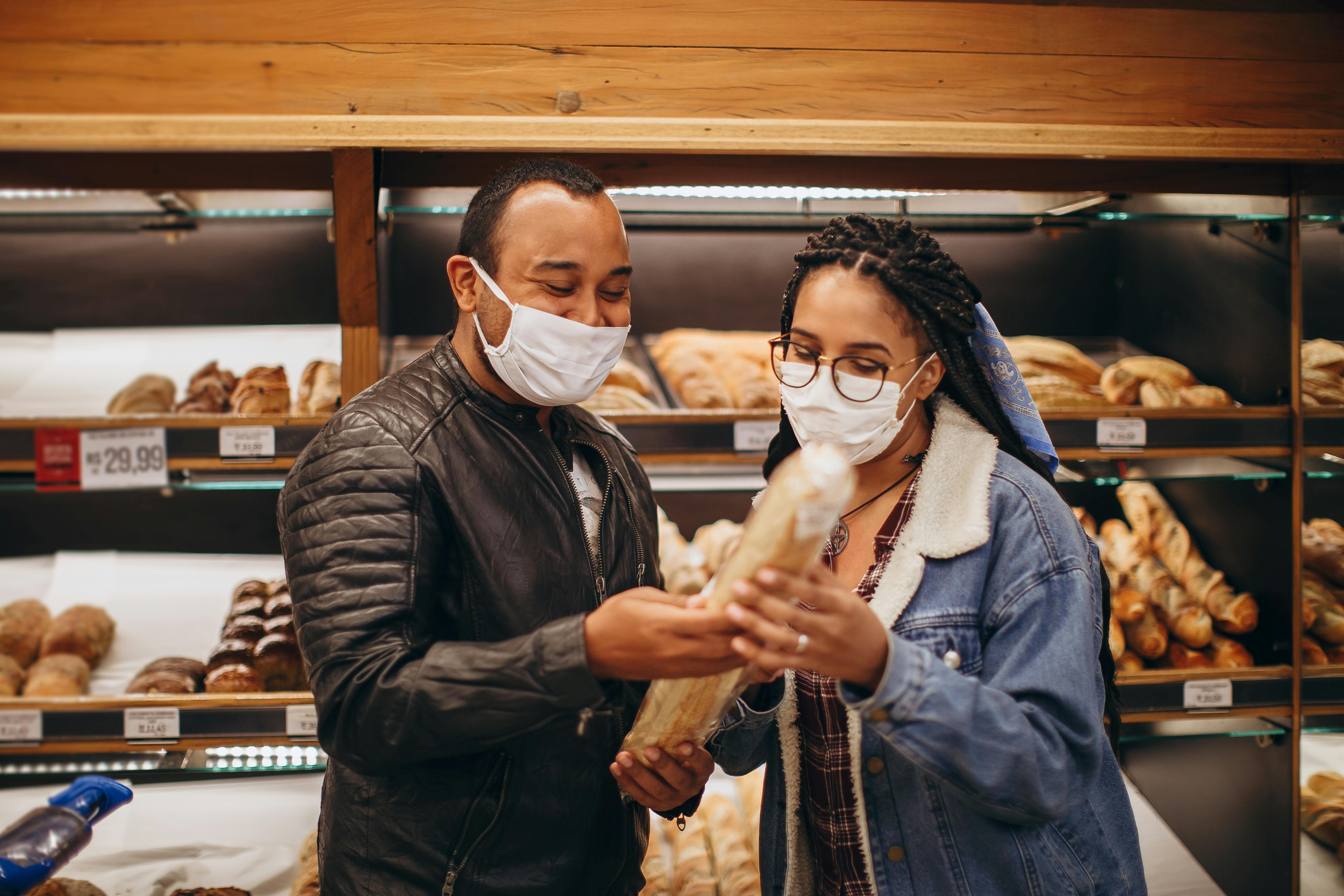 Man and Woman in Masks Holding Baguette at Supermarket · Free Stock Photo