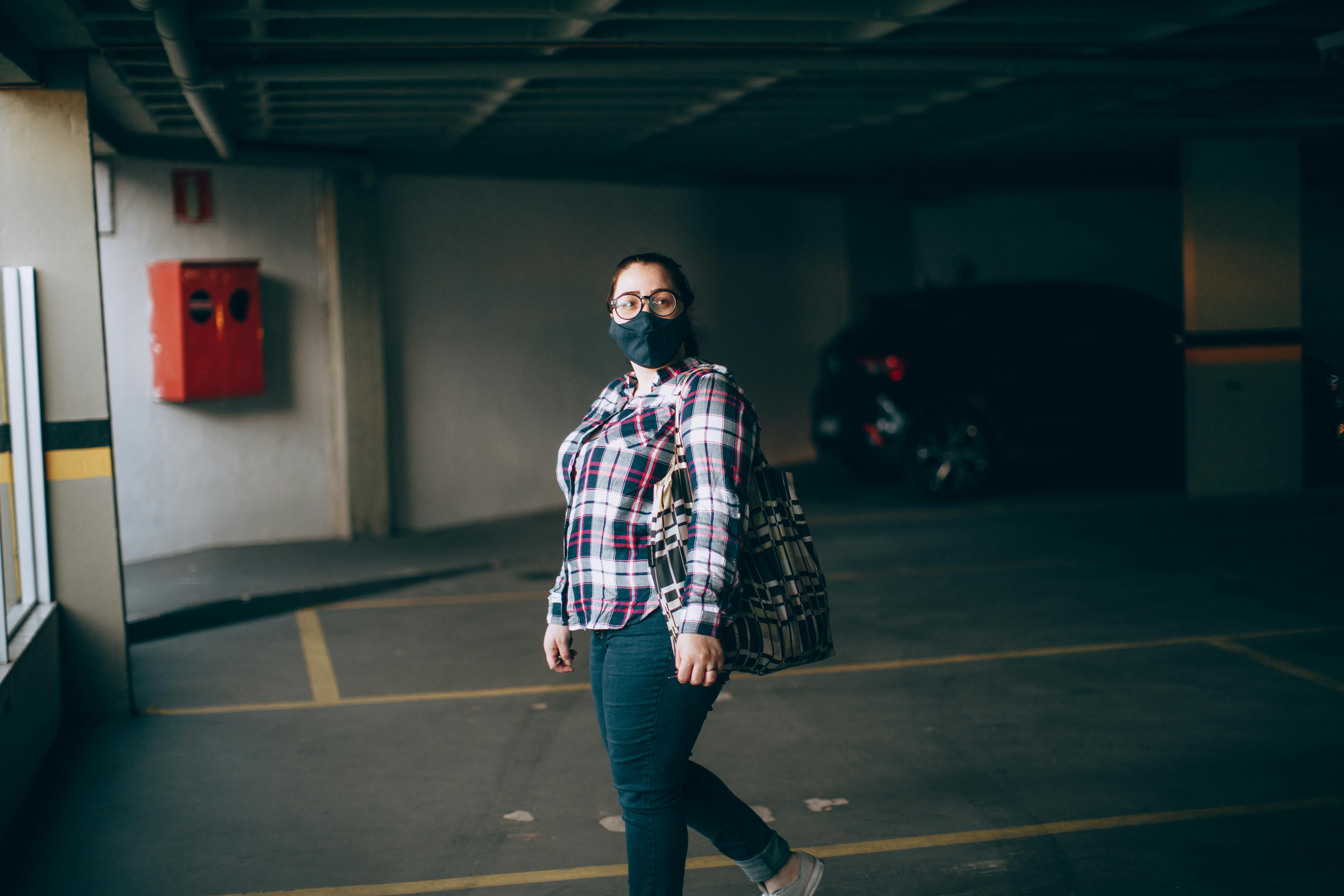 A woman wearing a face mask walks through a parking garage · Free Stock ...
