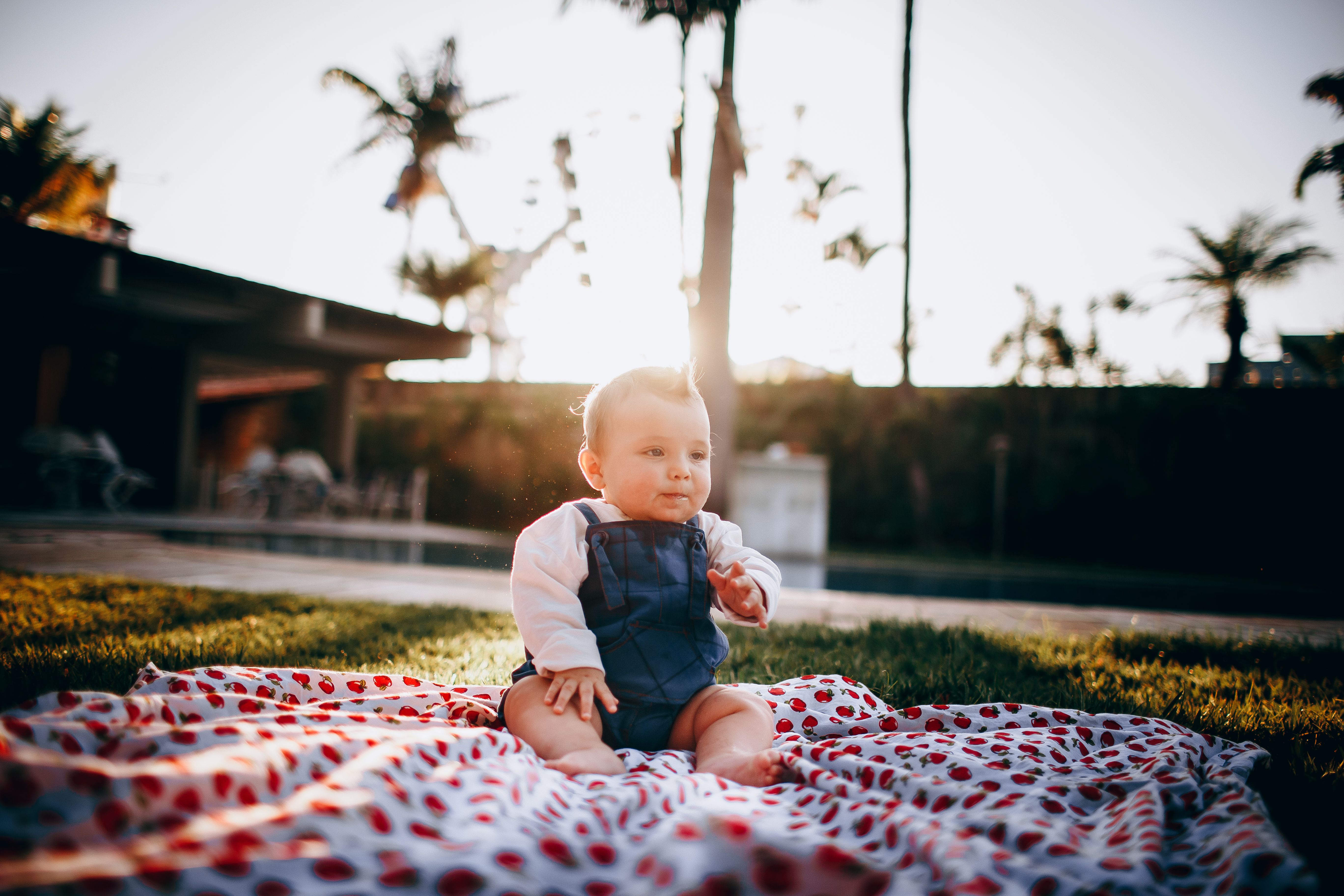 A baby sitting on a blanket in the sun · Free Stock Photo