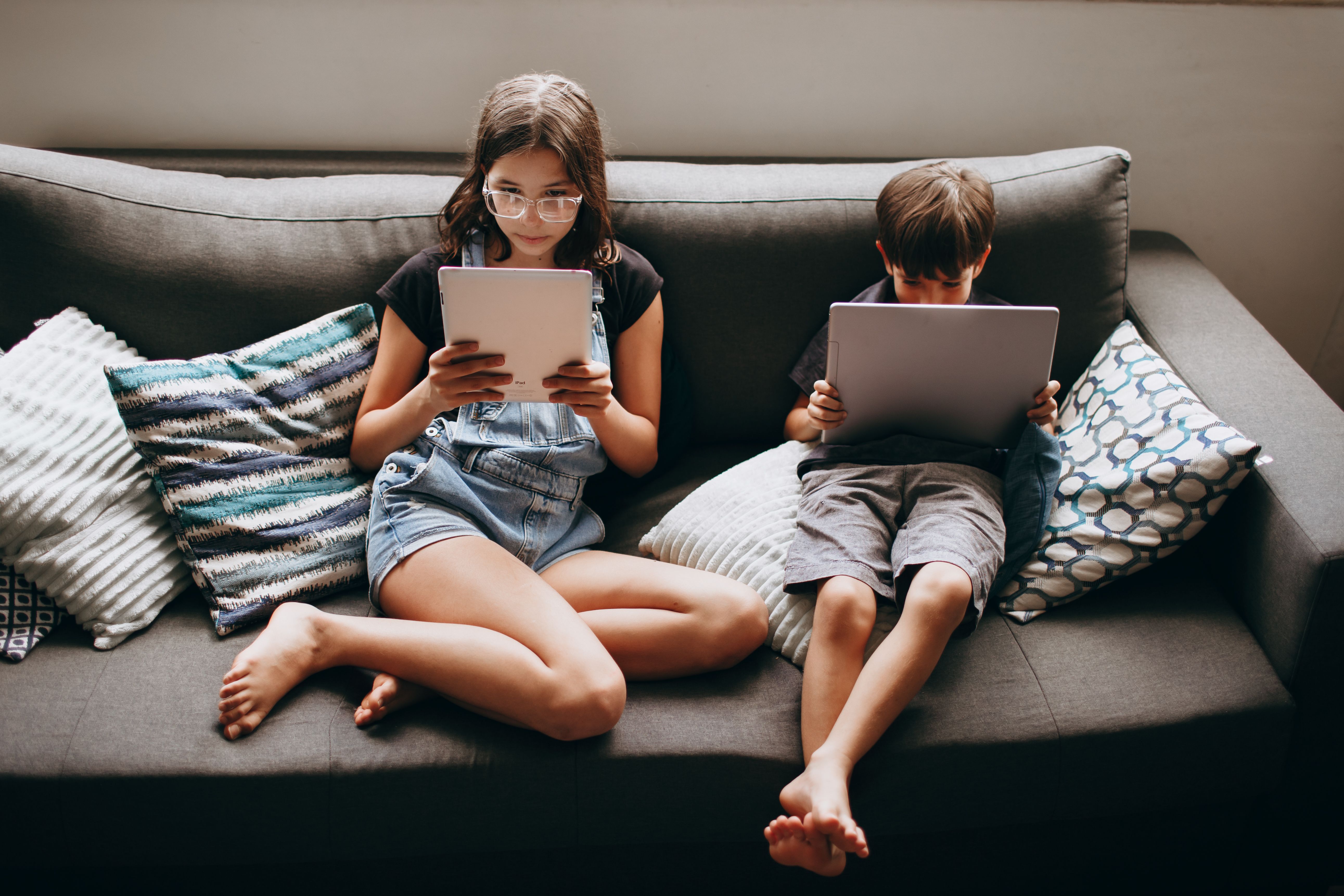 Two children sitting on a couch with their tablets · Free Stock Photo