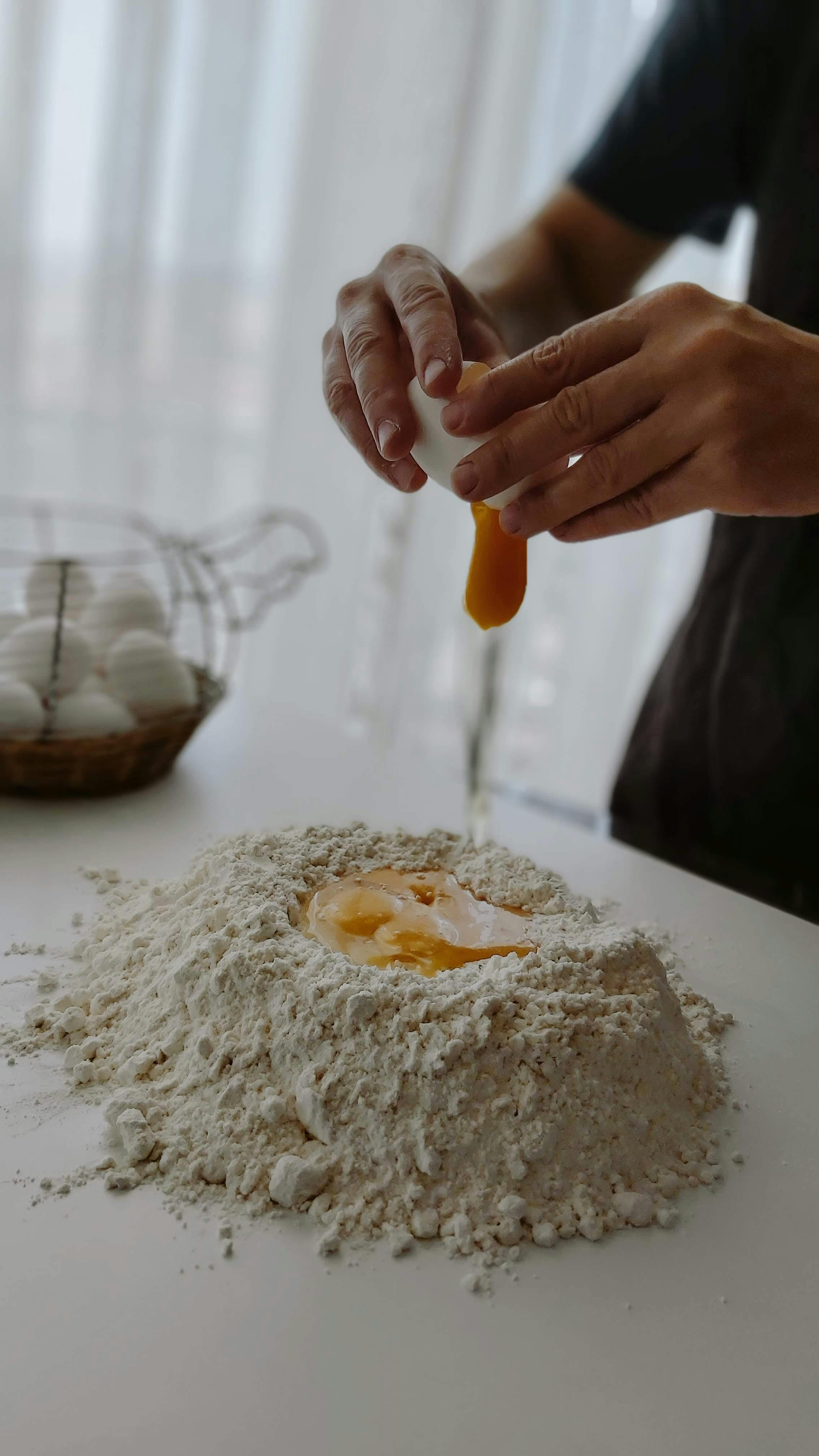 Crop cook breaking egg into flour · Free Stock Photo