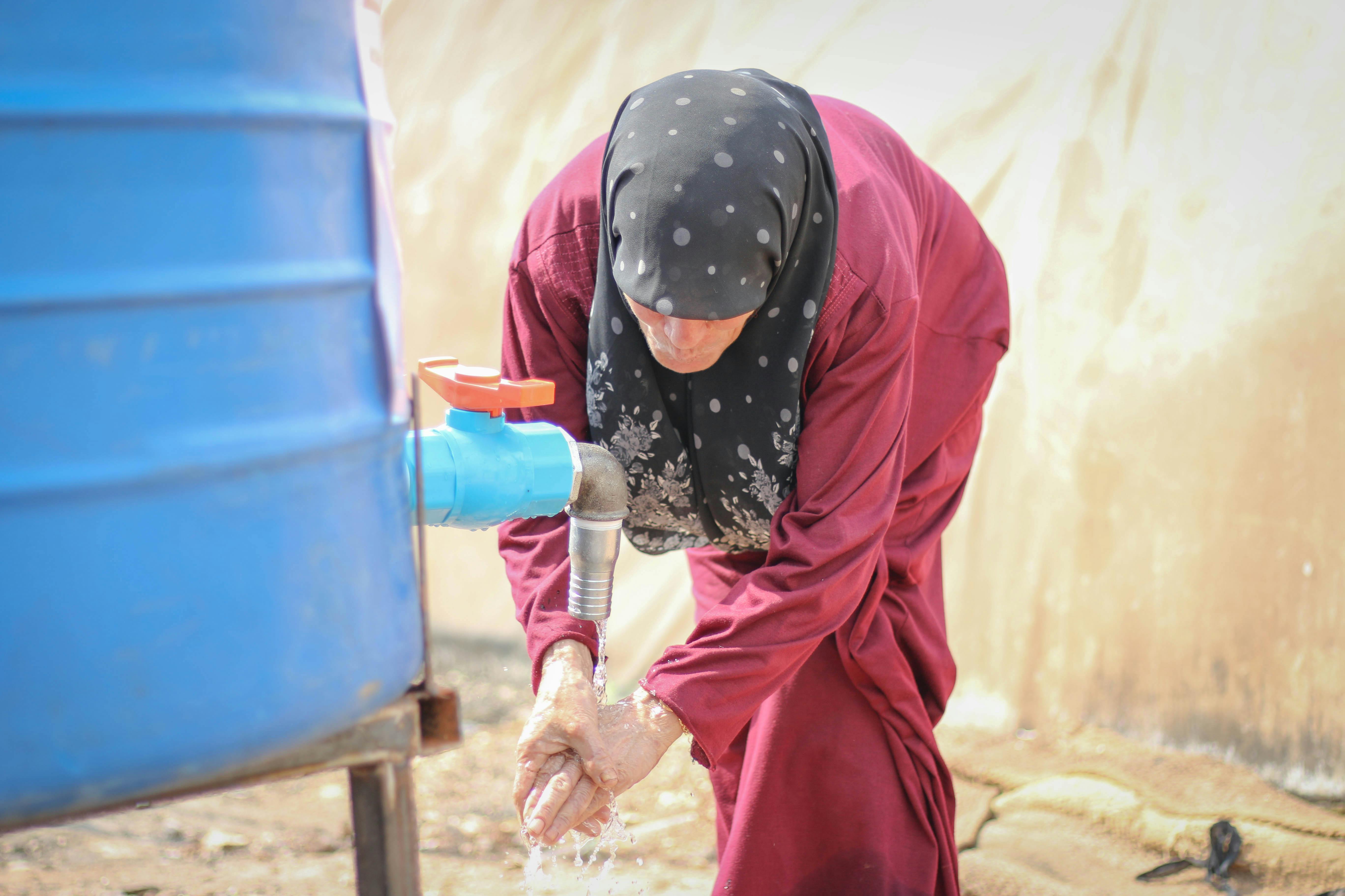 A woman in a hijab is filling water from a blue container · Free Stock ...