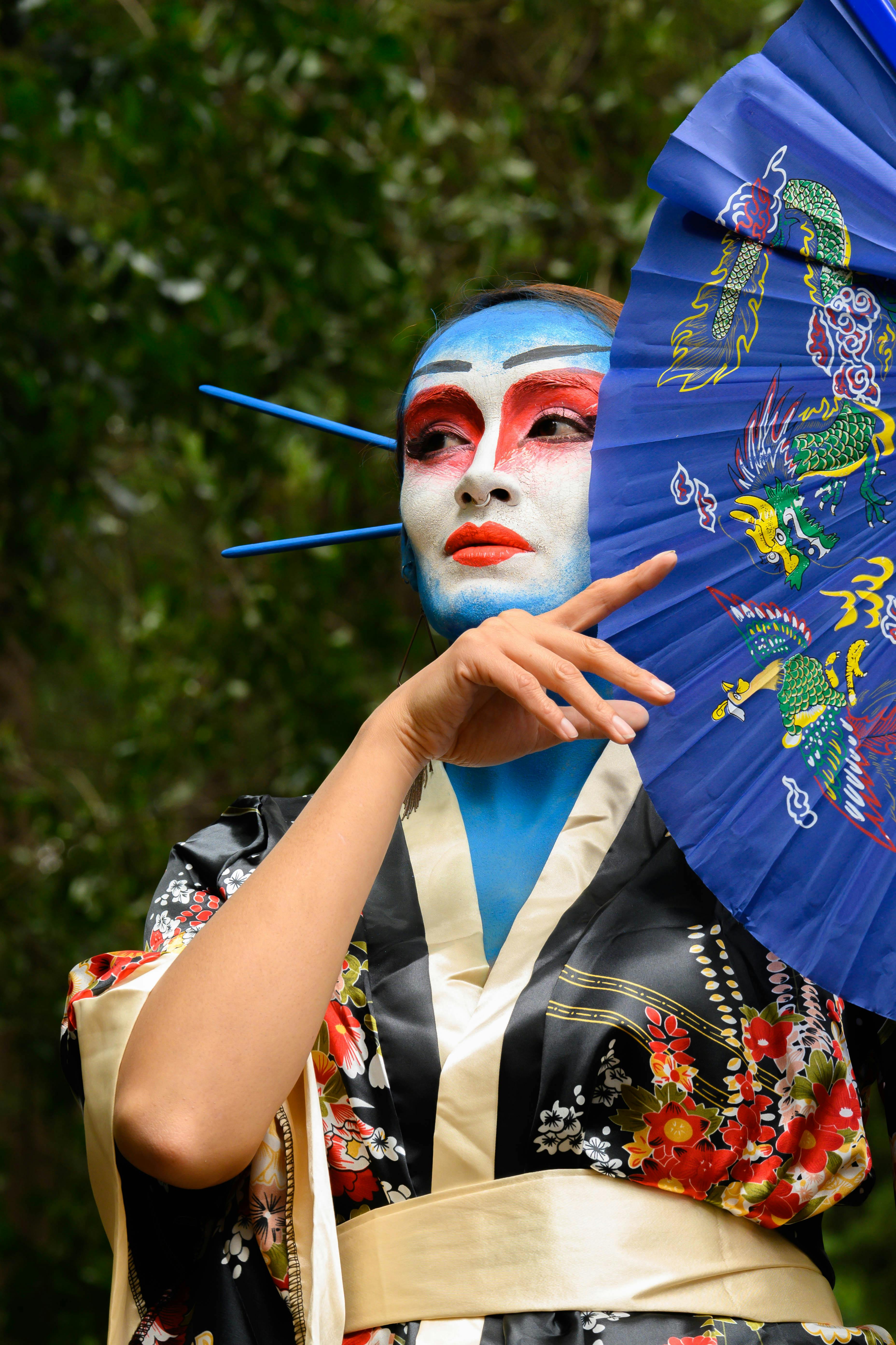 A woman with blue face paint holding a blue and white fan · Free Stock ...