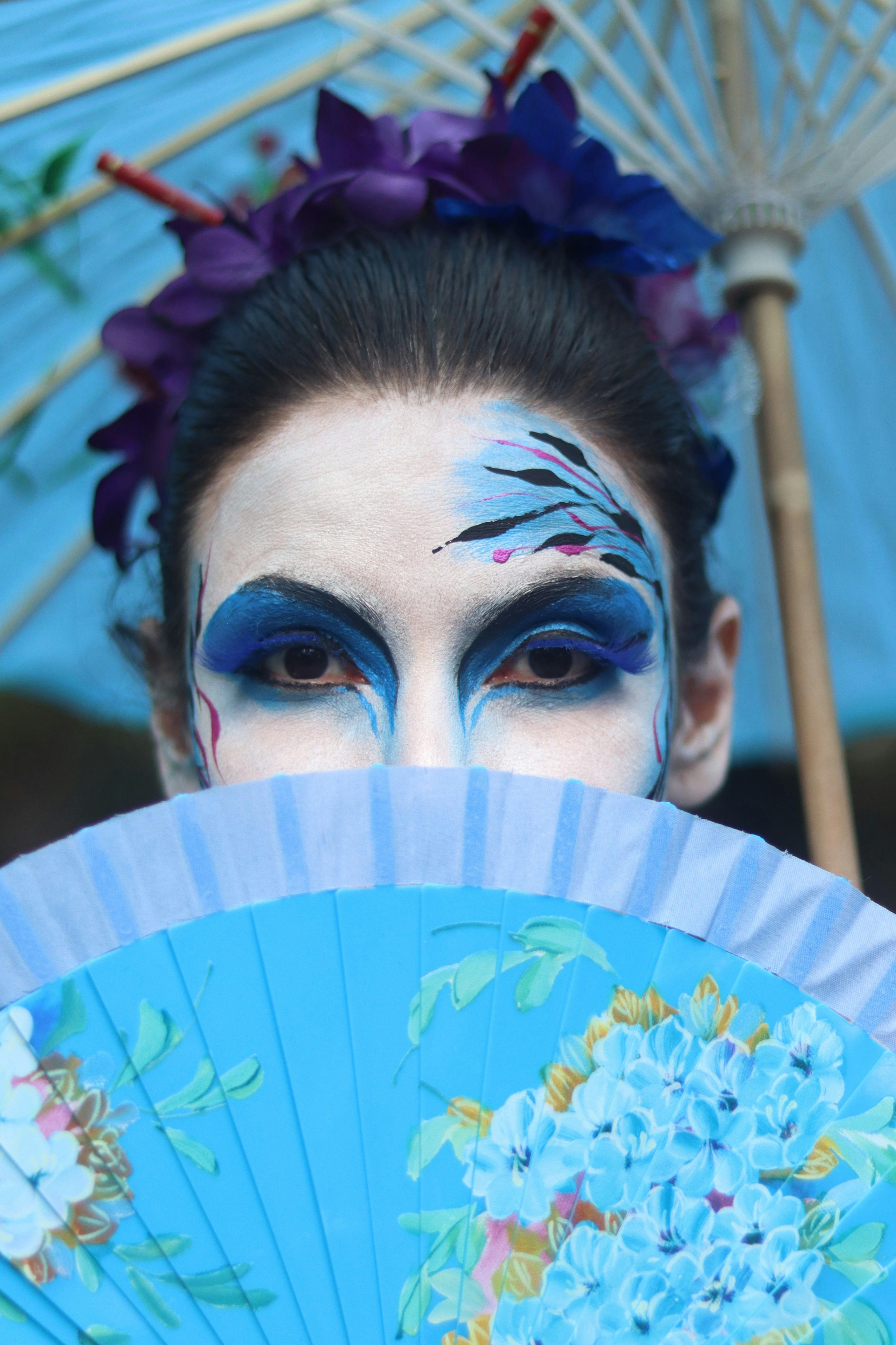 A woman with blue face paint and blue flowers holding a fan · Free ...