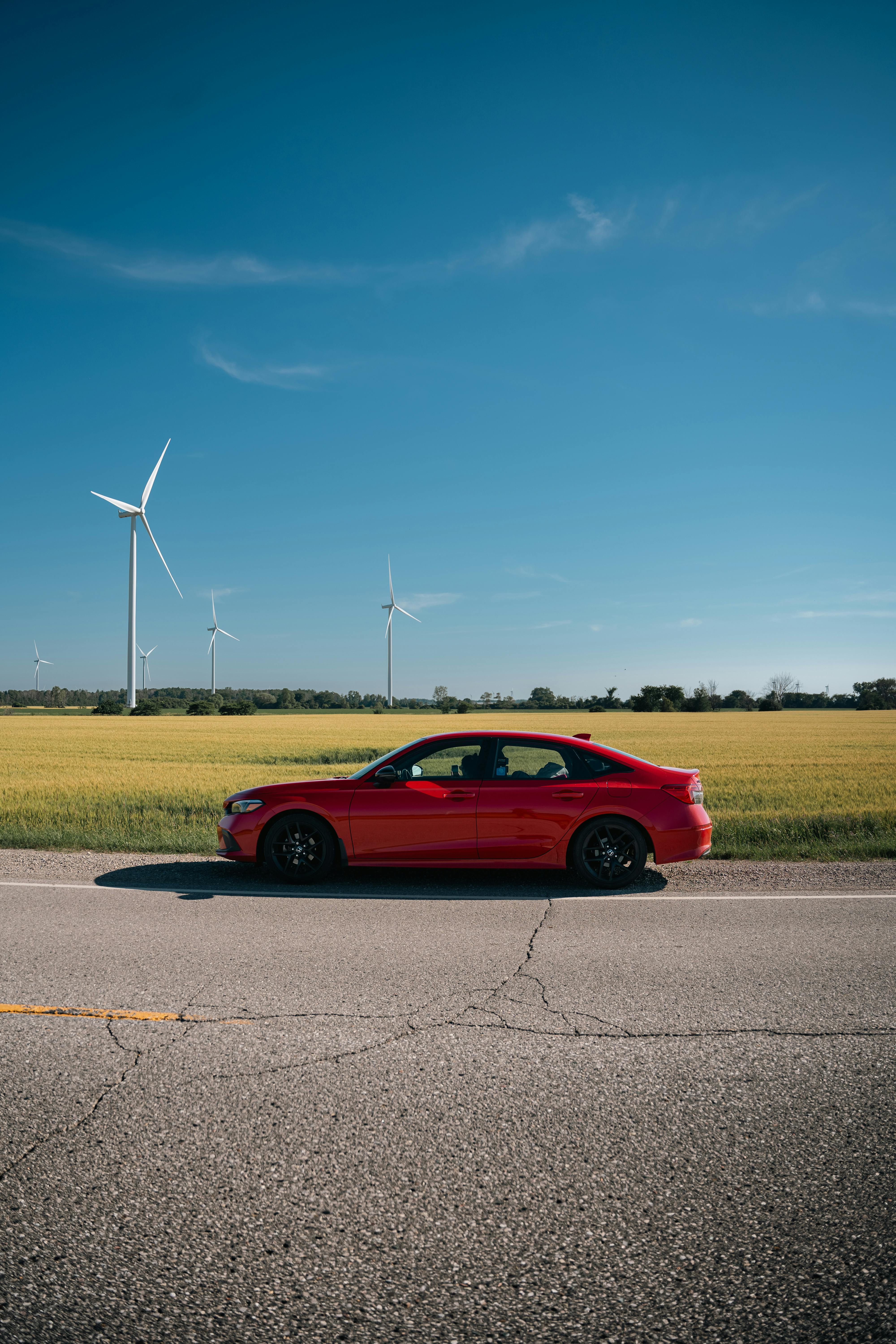 A red car driving down a road with wind turbines in the background ...