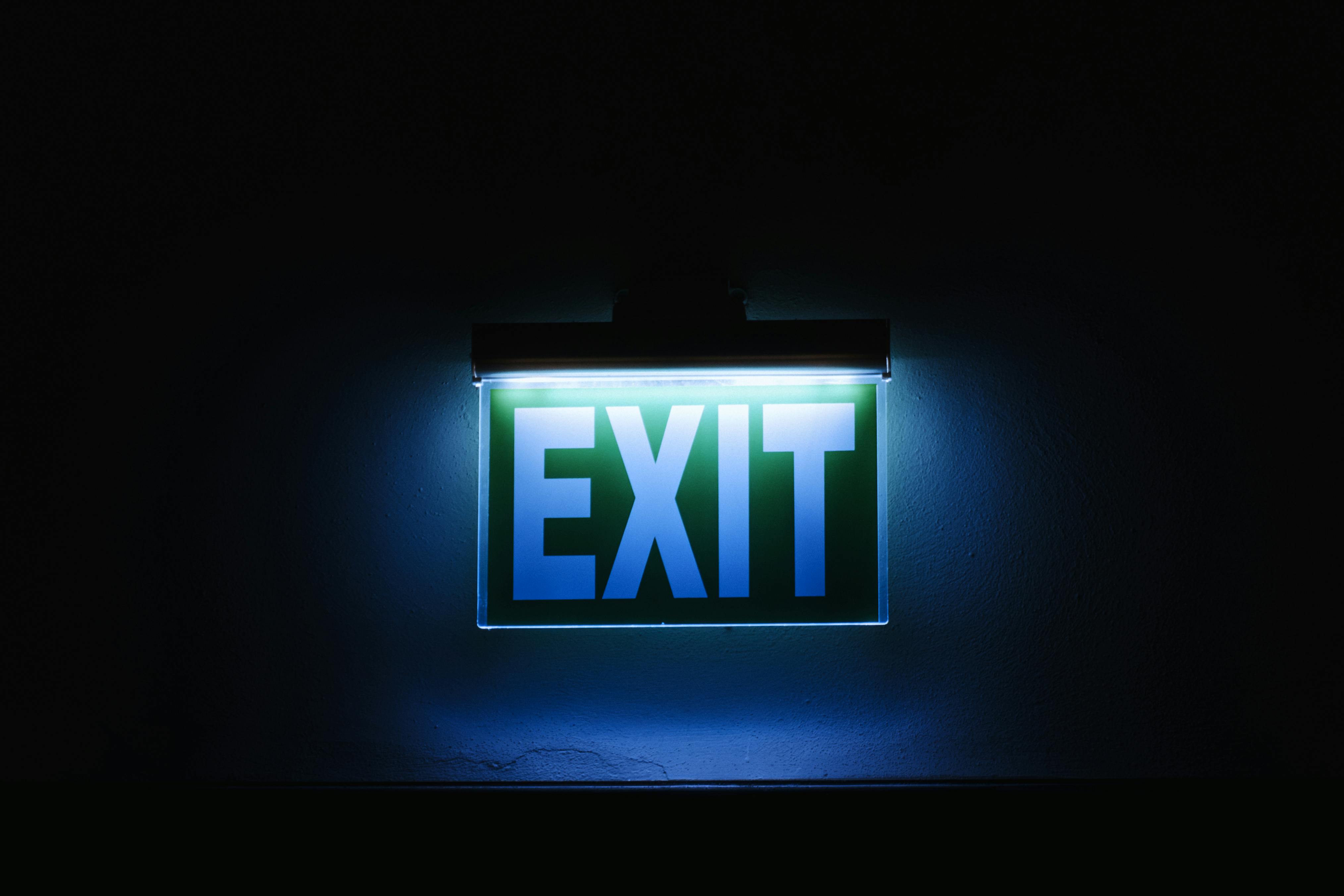 A blue exit sign lit up in the dark · Free Stock Photo