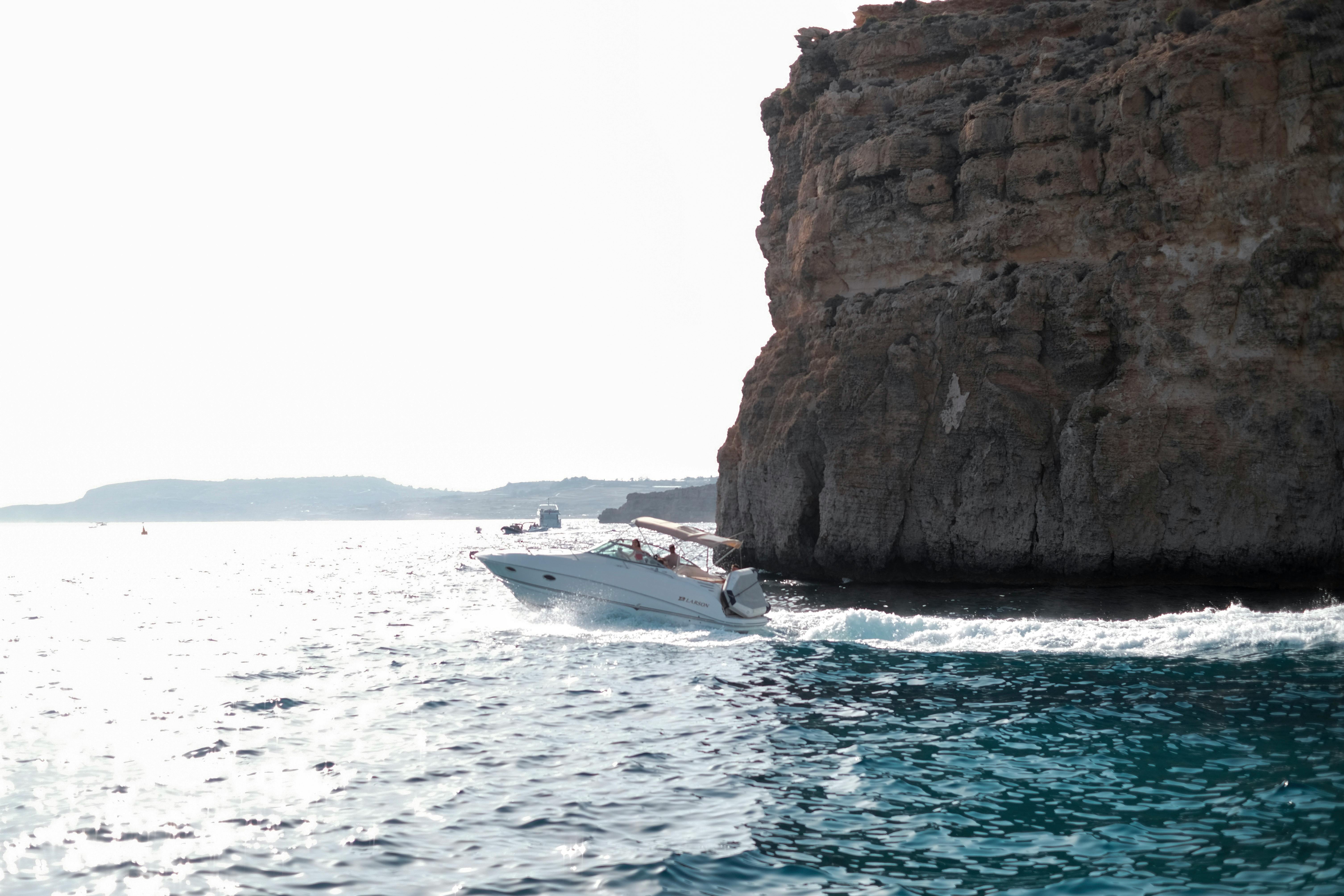 A boat is traveling through the water near a cliff · Free Stock Photo
