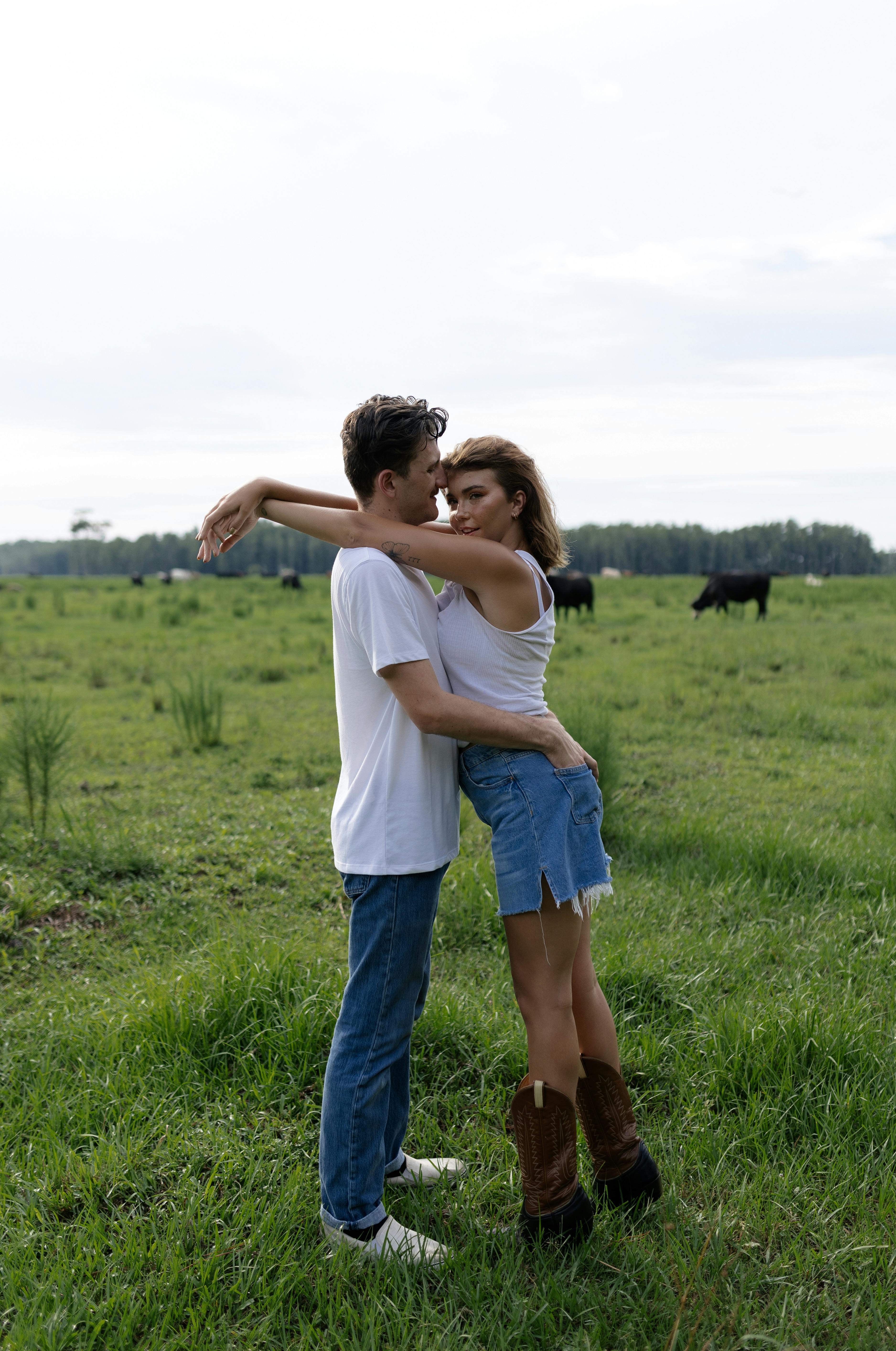 A couple hugging in a field with cows · Free Stock Photo