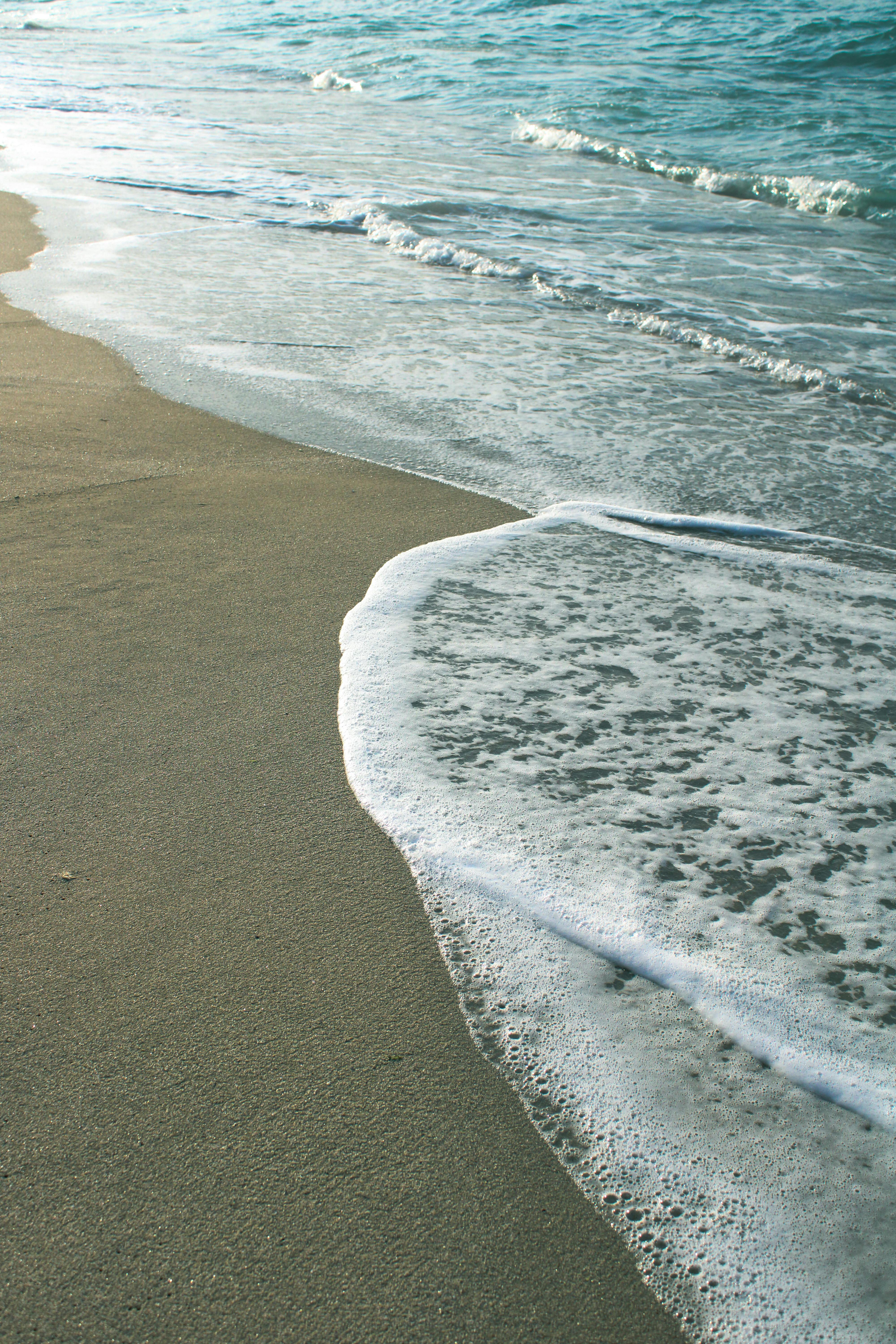 A beach with waves and sand on the shore · Free Stock Photo