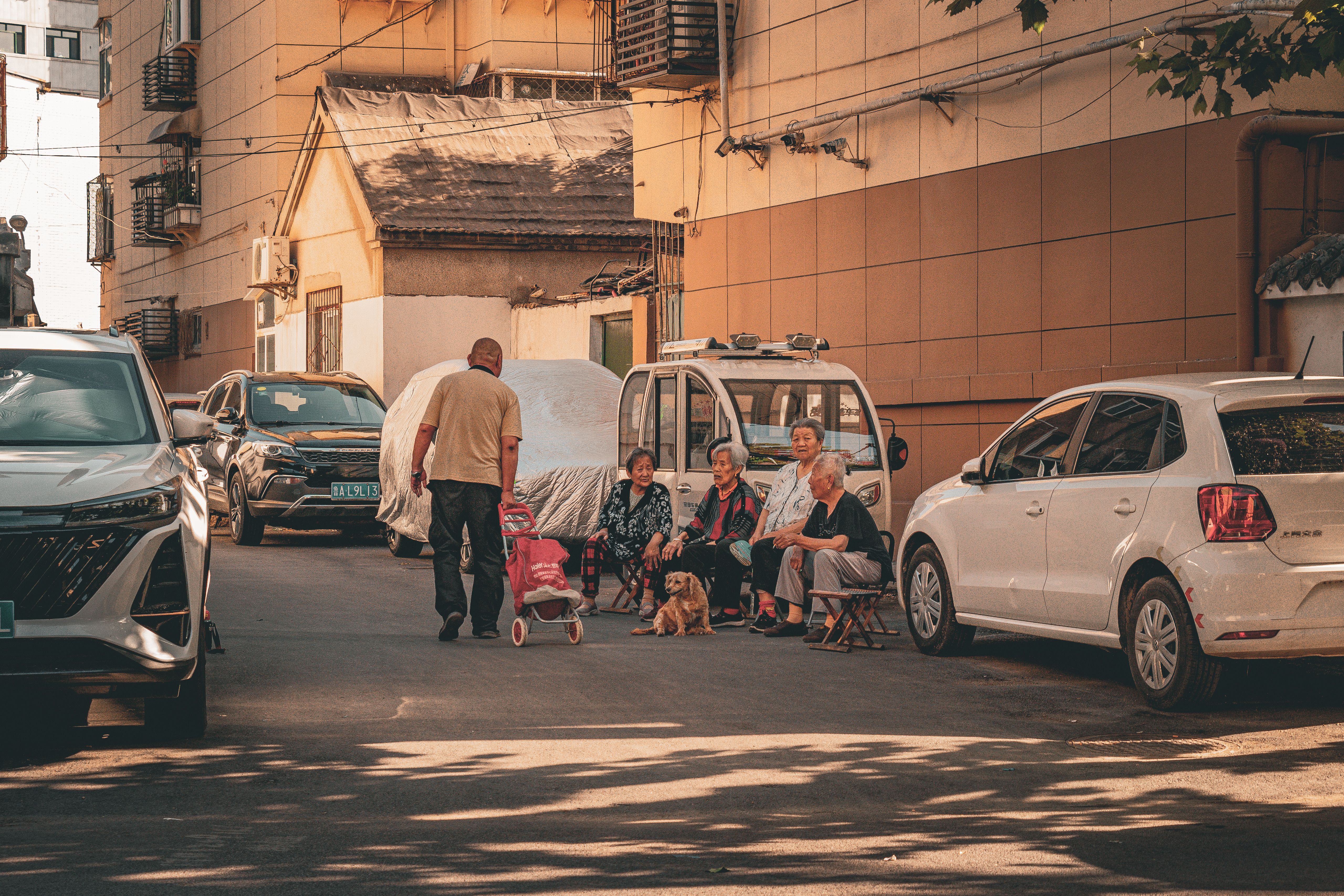 A group of people walking down a street with cars parked in the ...