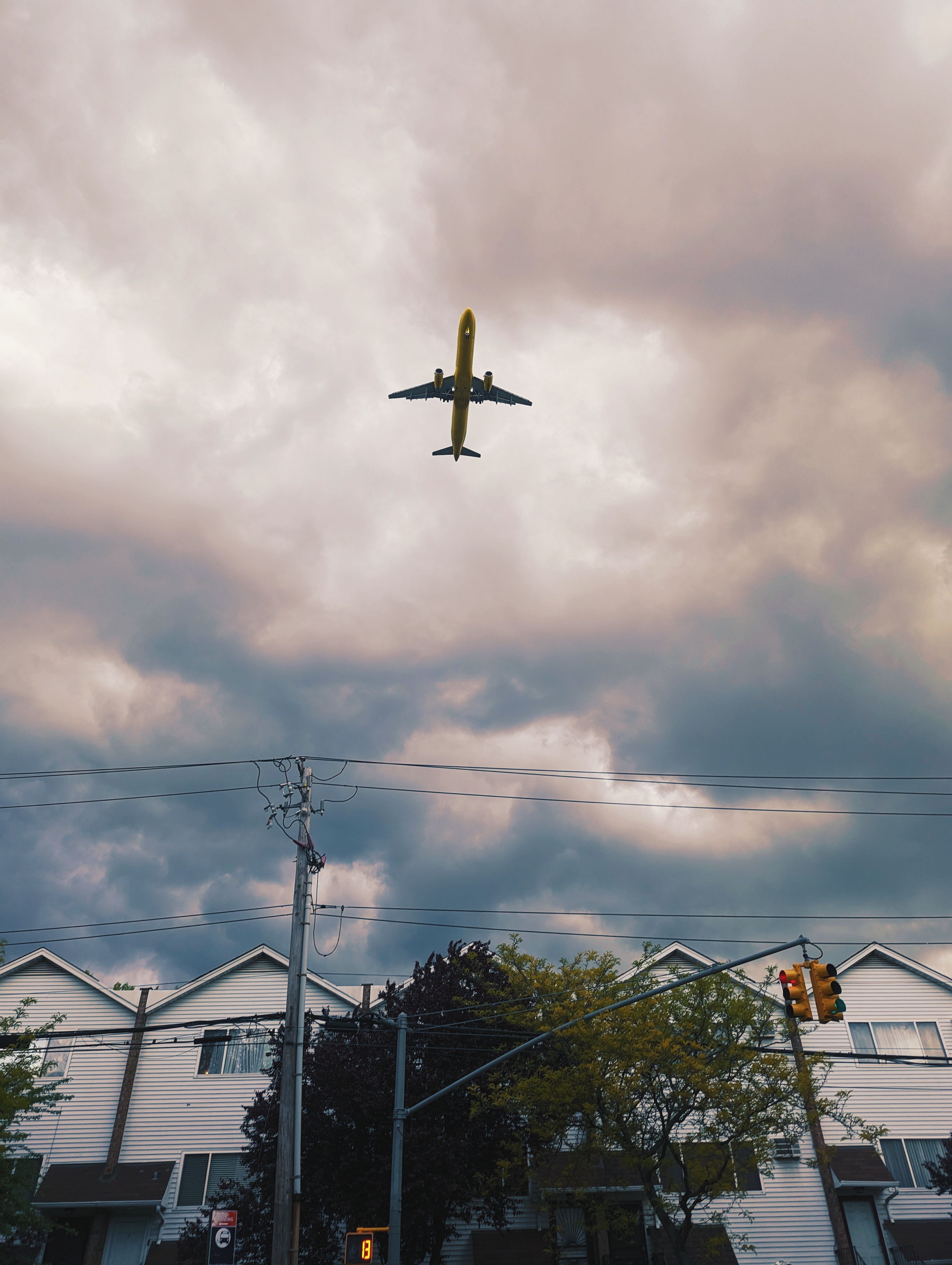 A plane flying over a city street with cloudy skies · Free Stock Photo