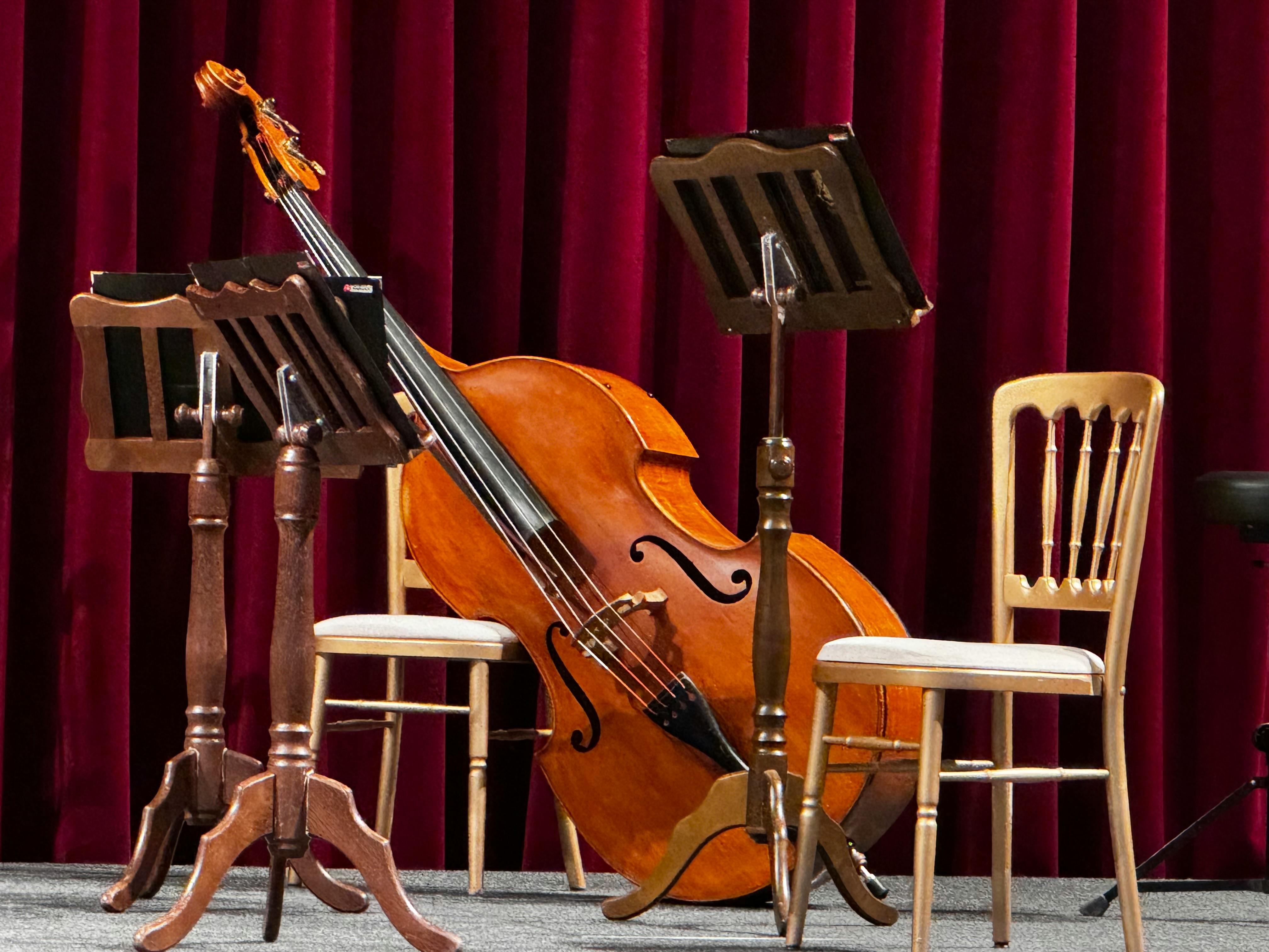 A cello and two chairs on stage with a music stand · Free Stock Photo